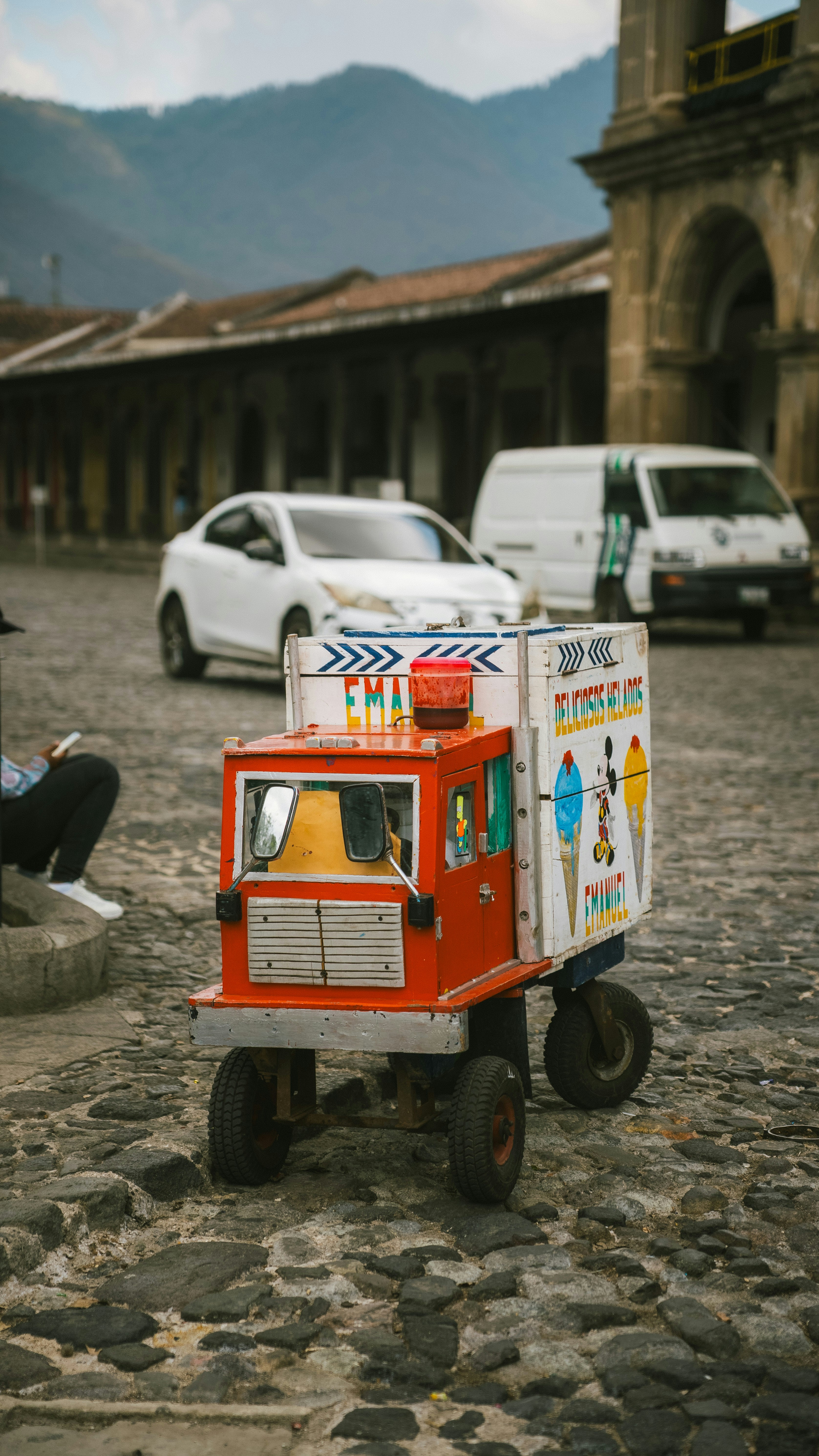 Cobbled Street Sentinel: A Red Toy Cart Among Historic Arches