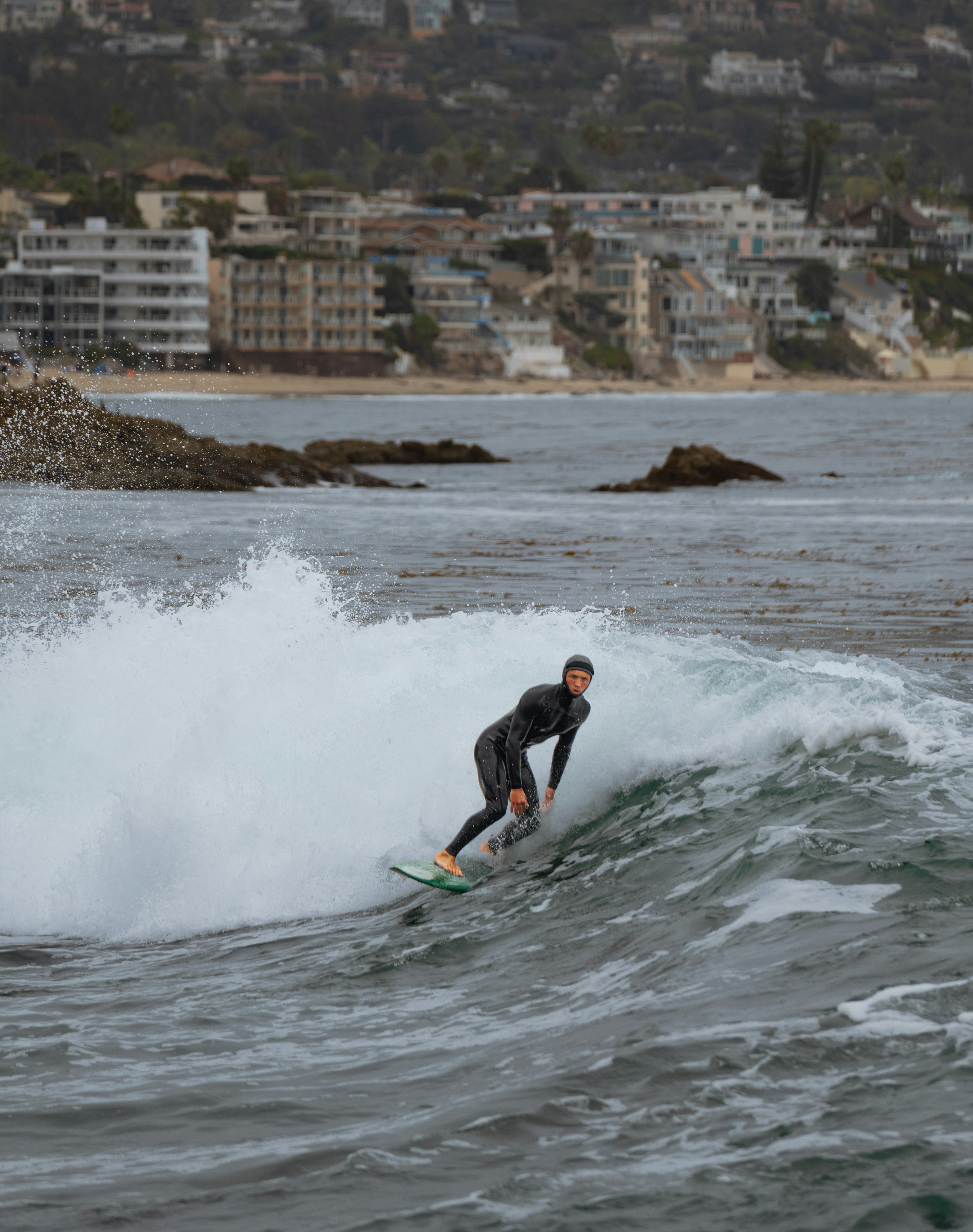 Carving the Crest: Surfer Navigates a Curl with a Distant Coastal City Backdrop