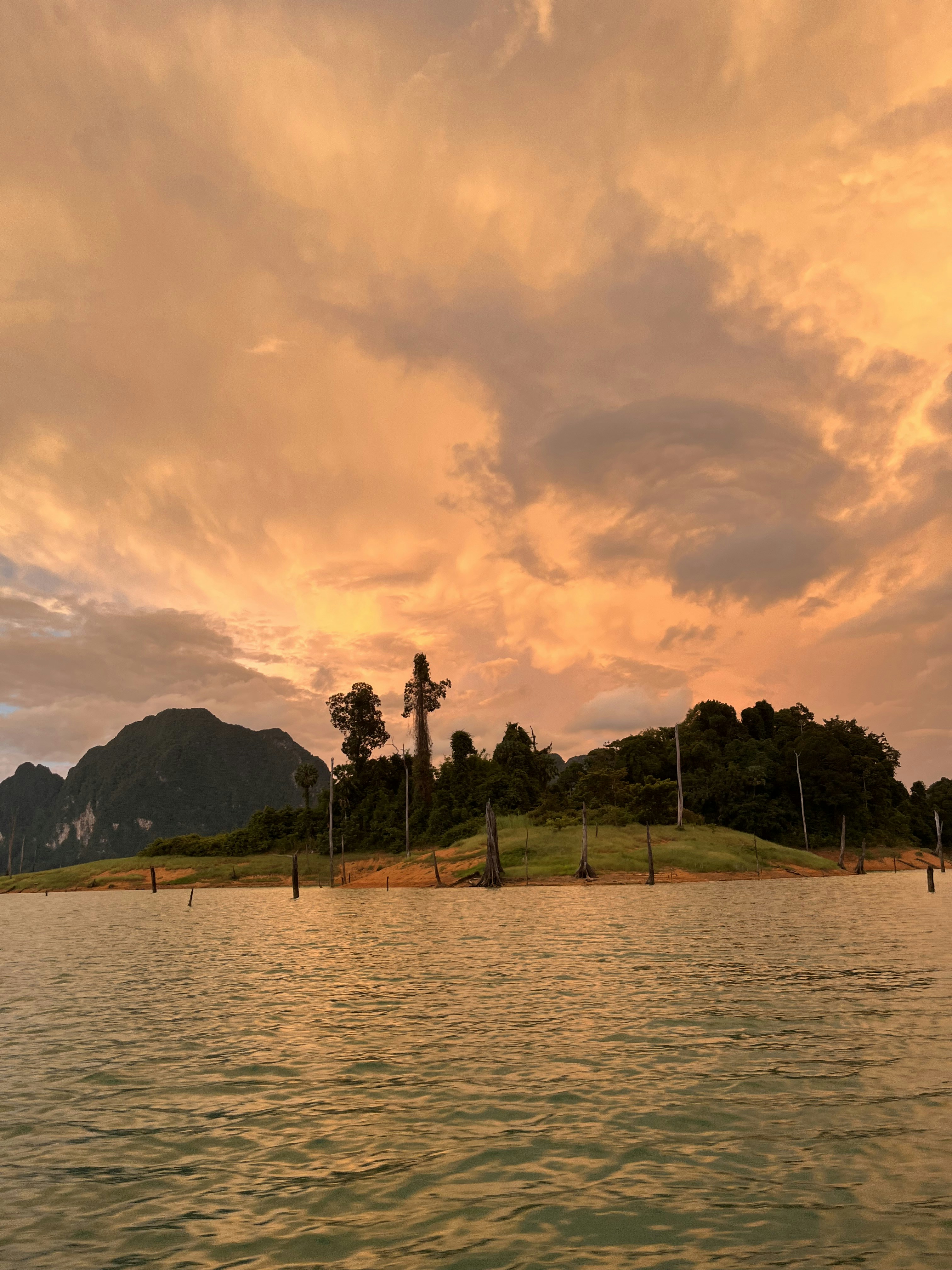 Dramatic clouds illuminated by sunset hues over a calm lake with a tree-lined island.