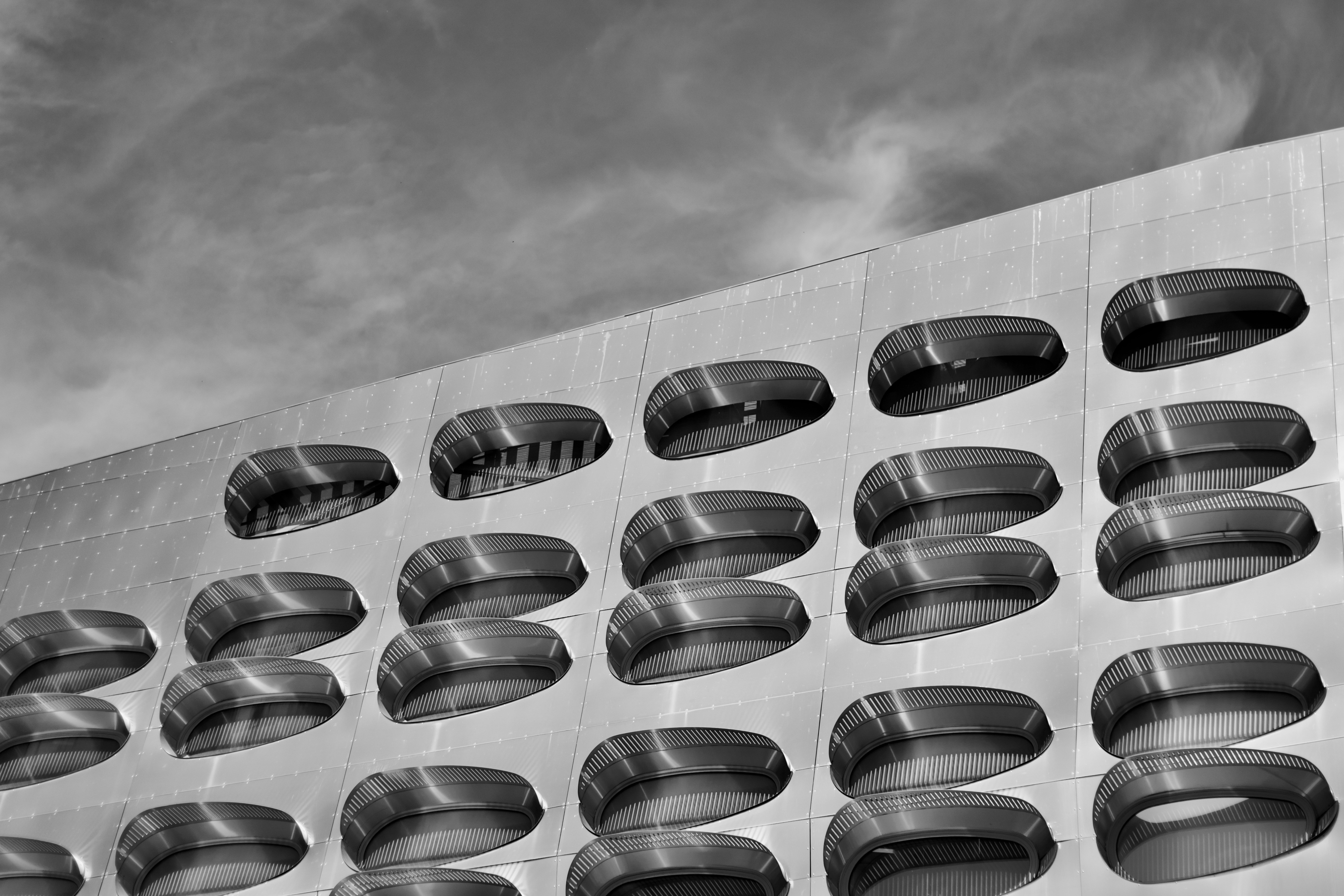 Abstract architectural detail showcasing a series of oval openings on a metallic surface, emphasizing patterns and textures. Black and white tones enhance the visual impact.