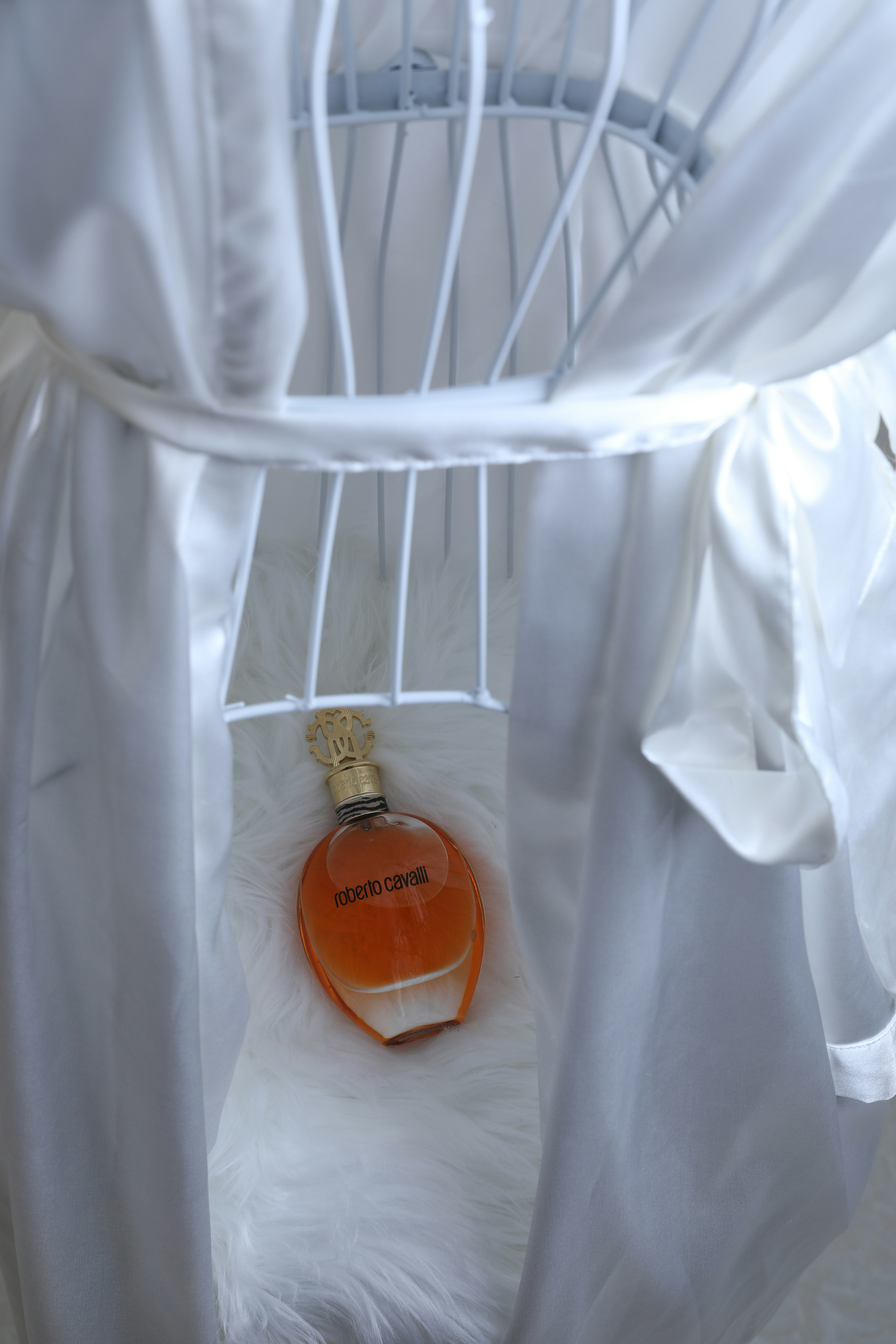 Frayed white curtains cradle a framed amber perfume bottle