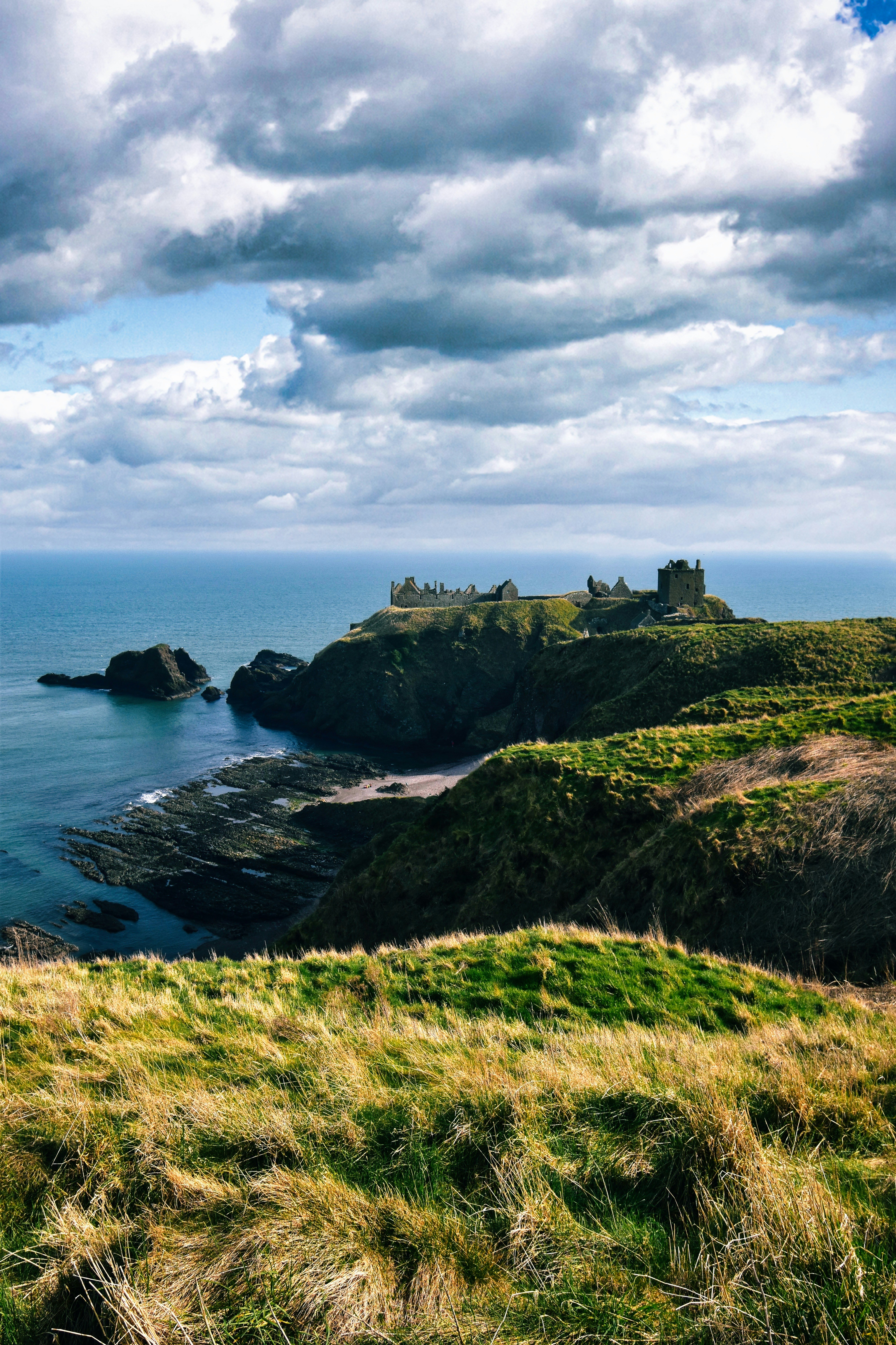 Dunnottar Castle is a ruined medieval fortress located upon a rocky headland on the northeast coast of Scotland, south of Stonehaven in Aberdeenshire. | Castle ruins sit atop a rugged coastal cliff.