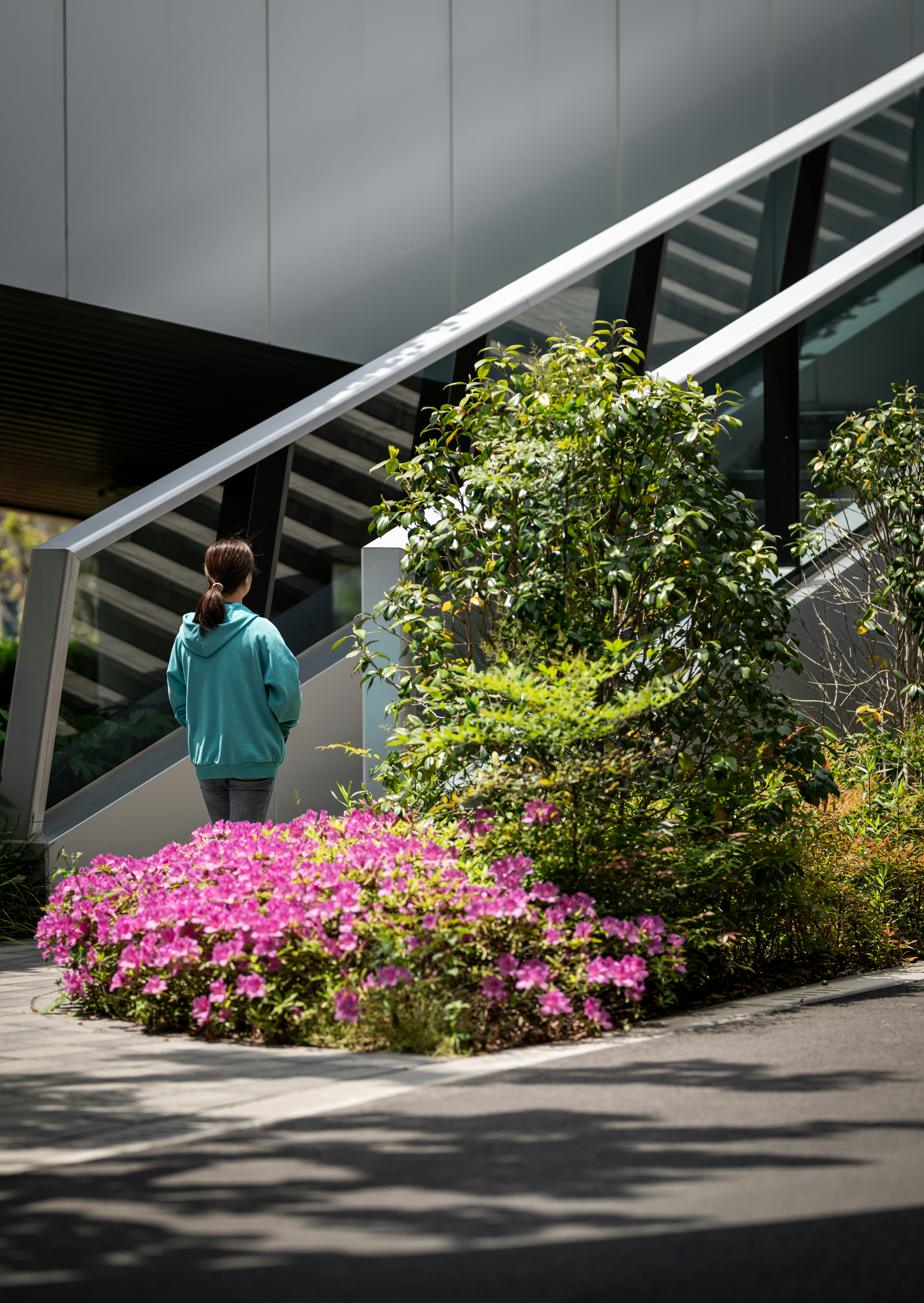 Teal-clad figure by the glass escalator amid vibrant garden blooms