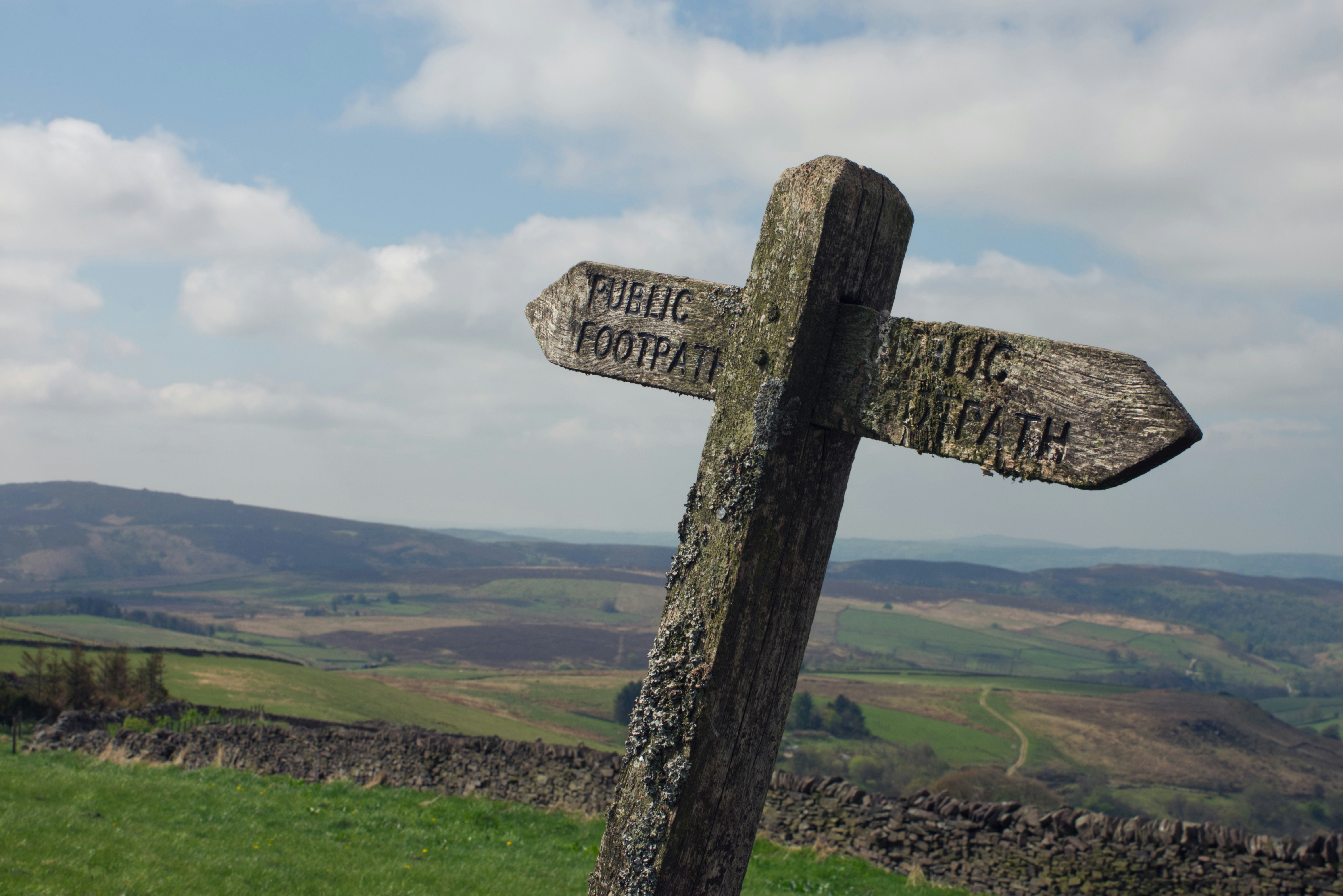 Close up of an old public footpath sign at Three Shires Head, Buxton, UK. | Wooden signpost directs to a scenic hiking trail.