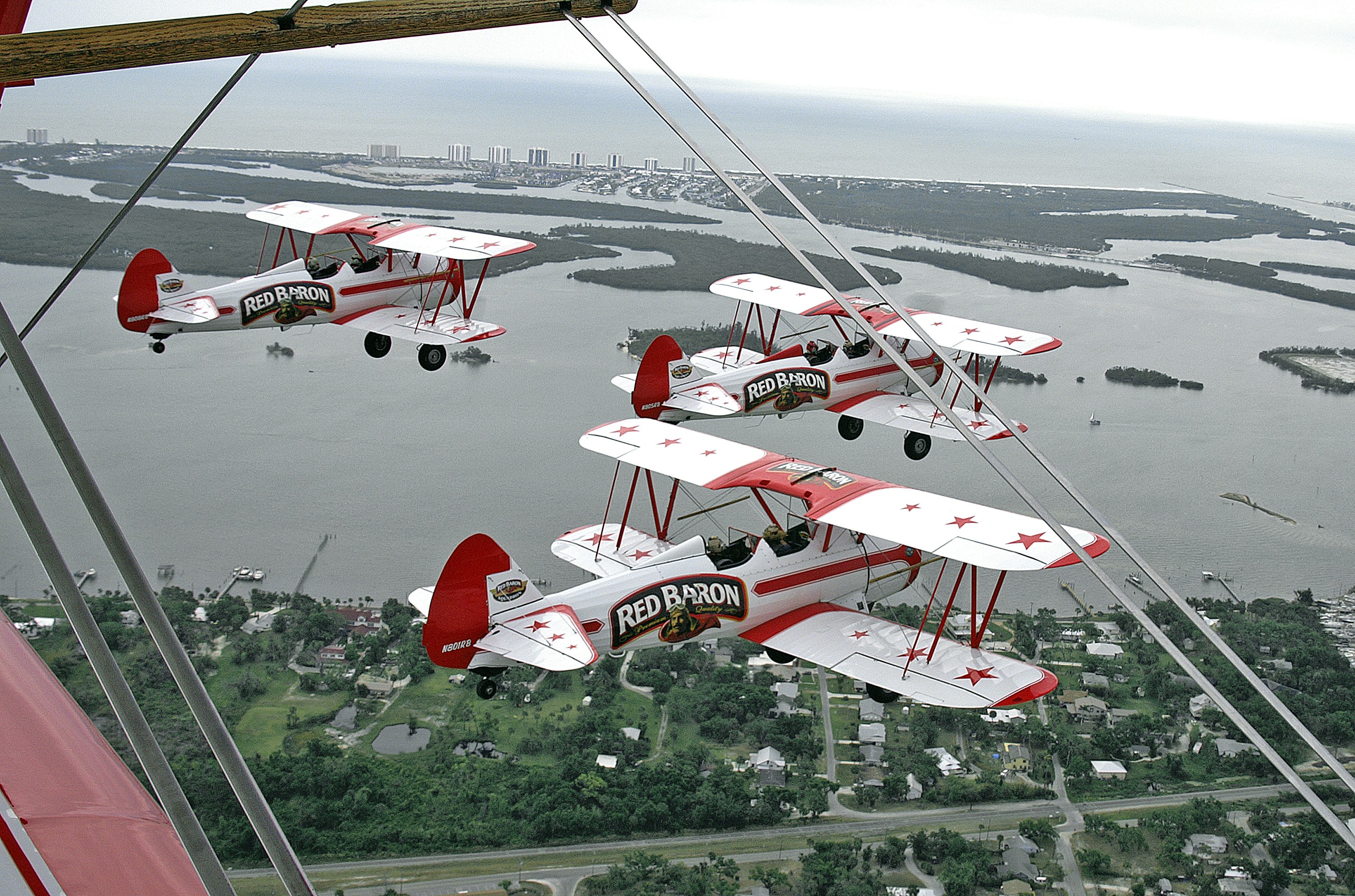 Four biplanes fly in formation over a coastal landscape. photo – Free ...