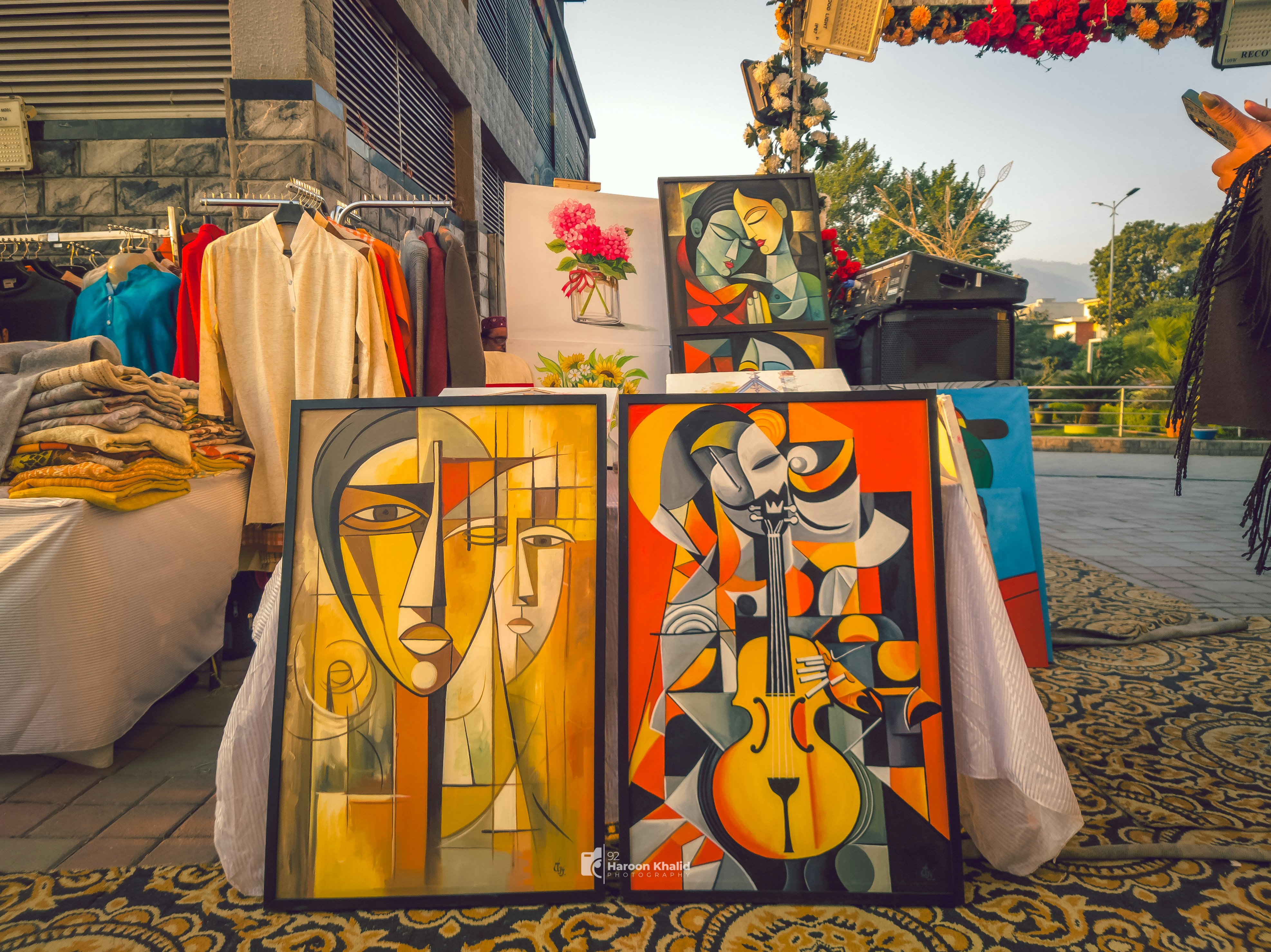 A surreal, abstract artwork capturing the essence of a face through fragmented, cubist-style shapes reminiscent of Picasso's influence. The use of bold, layered textures and geometric color blocks creates a striking visual that feels both artistic and emotional, evoking depth and curiosity. | Art is displayed at an outdoor market.