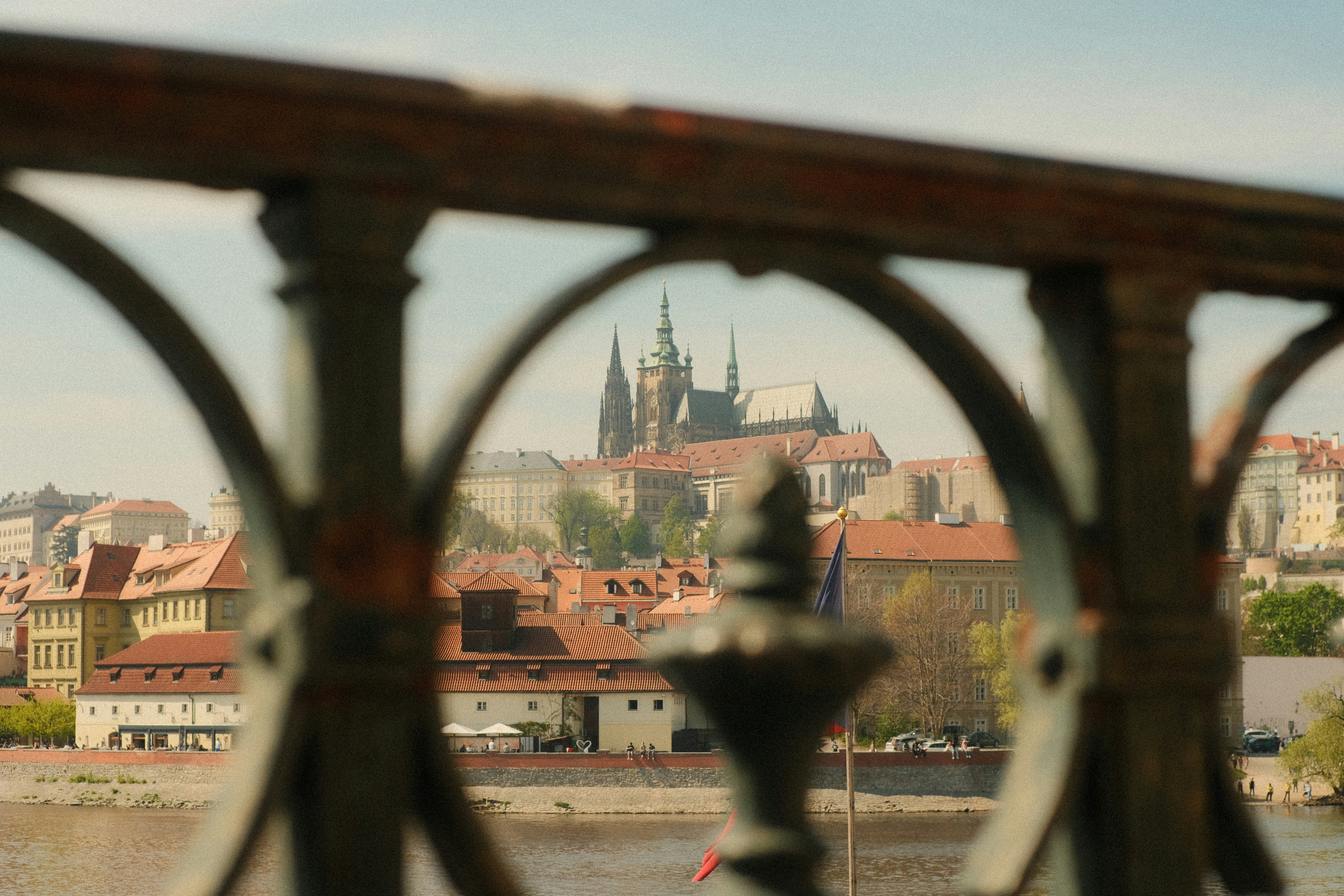 View of Prague Castle through ornate metalwork, highlighting the architectural beauty against a clear sky.