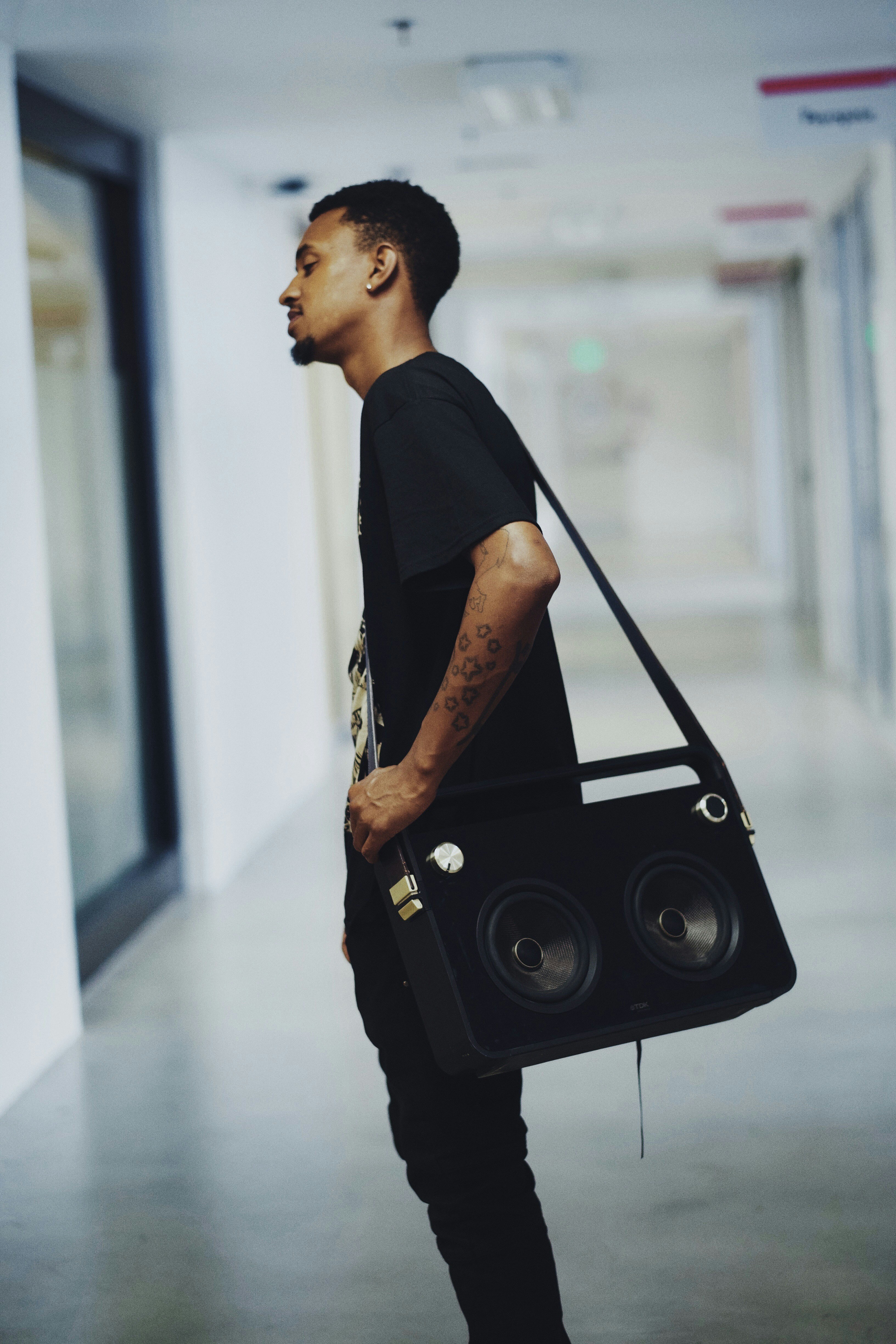 Transit Bass: Portrait of a Man Carrying a Giant Speaker Bag Through a Bright Hallway