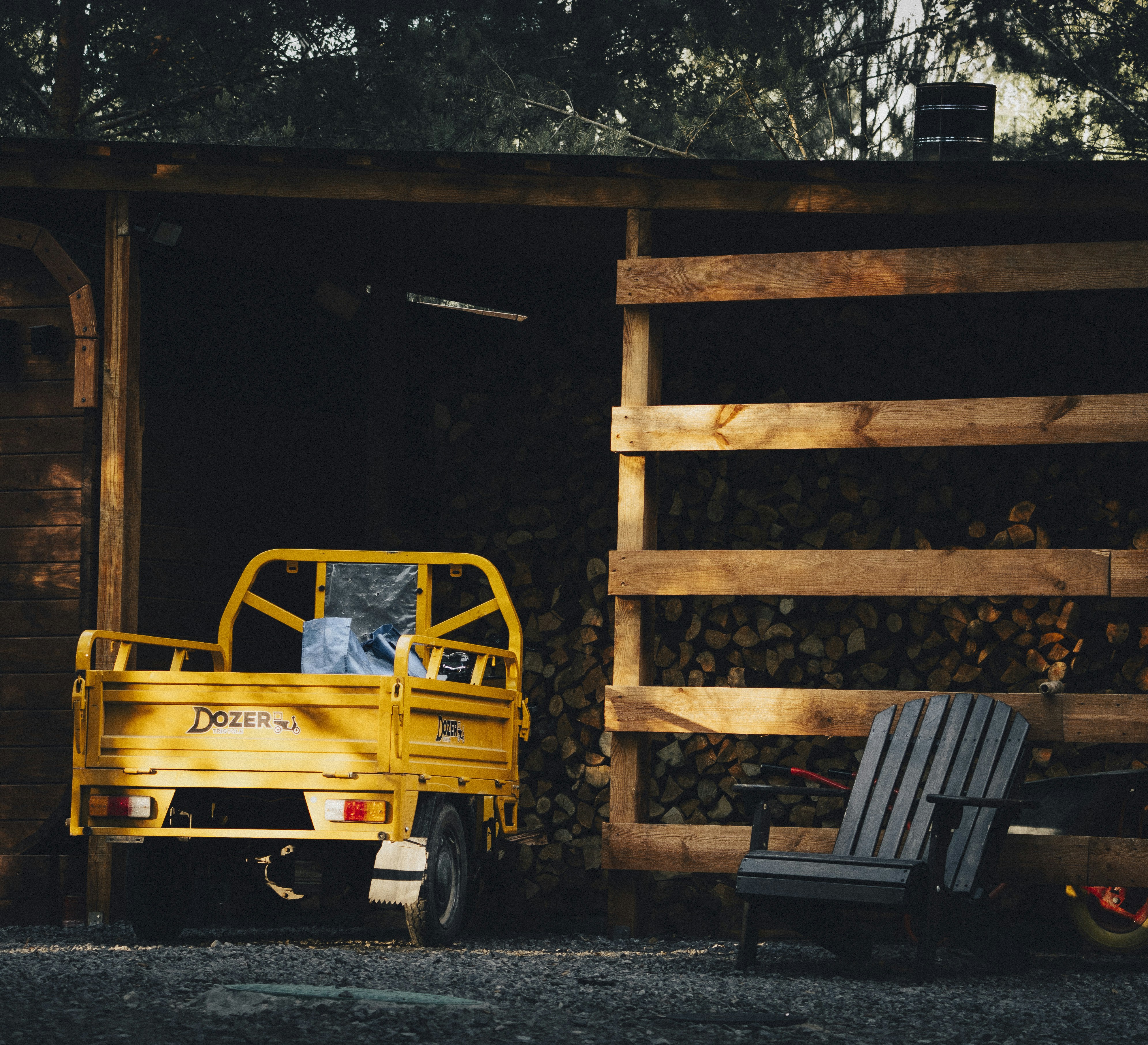 Yellow utility trailer at dusk beside stacked timber and chair