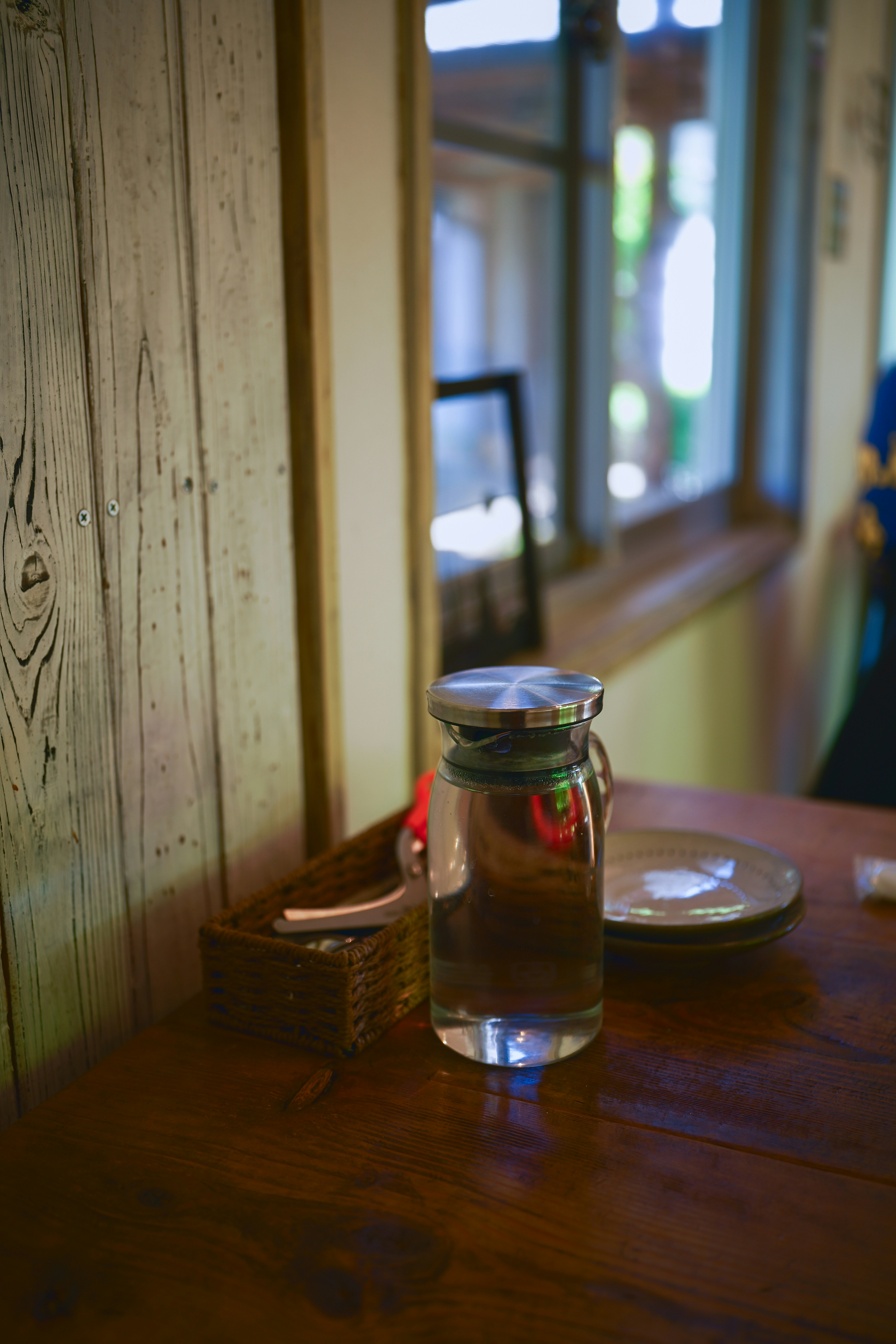 Clear glass water jar beside a woven basket on a wooden table, with soft natural light illuminating the scene.