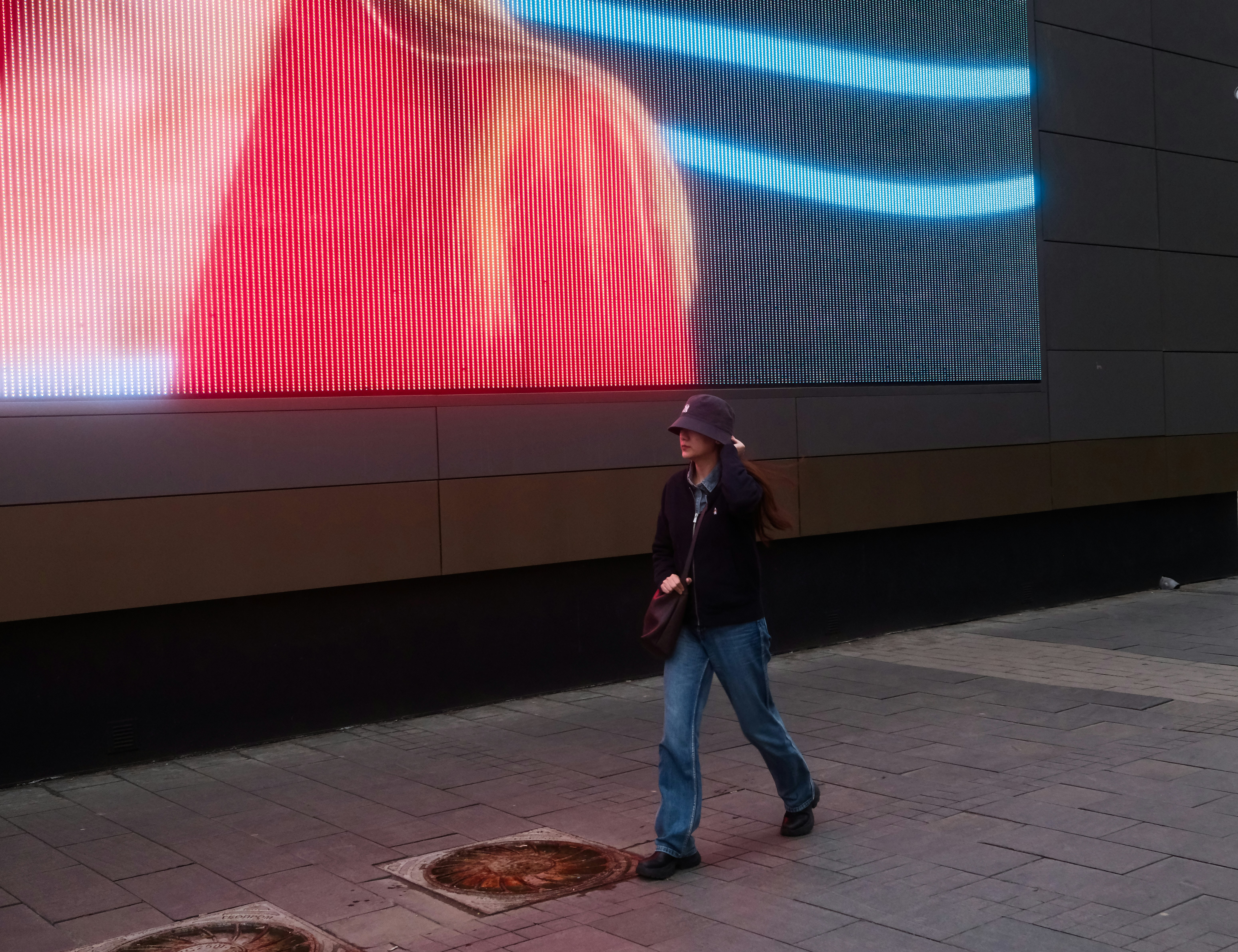 Pedestrian crossing a modern plaza with a giant LED panel