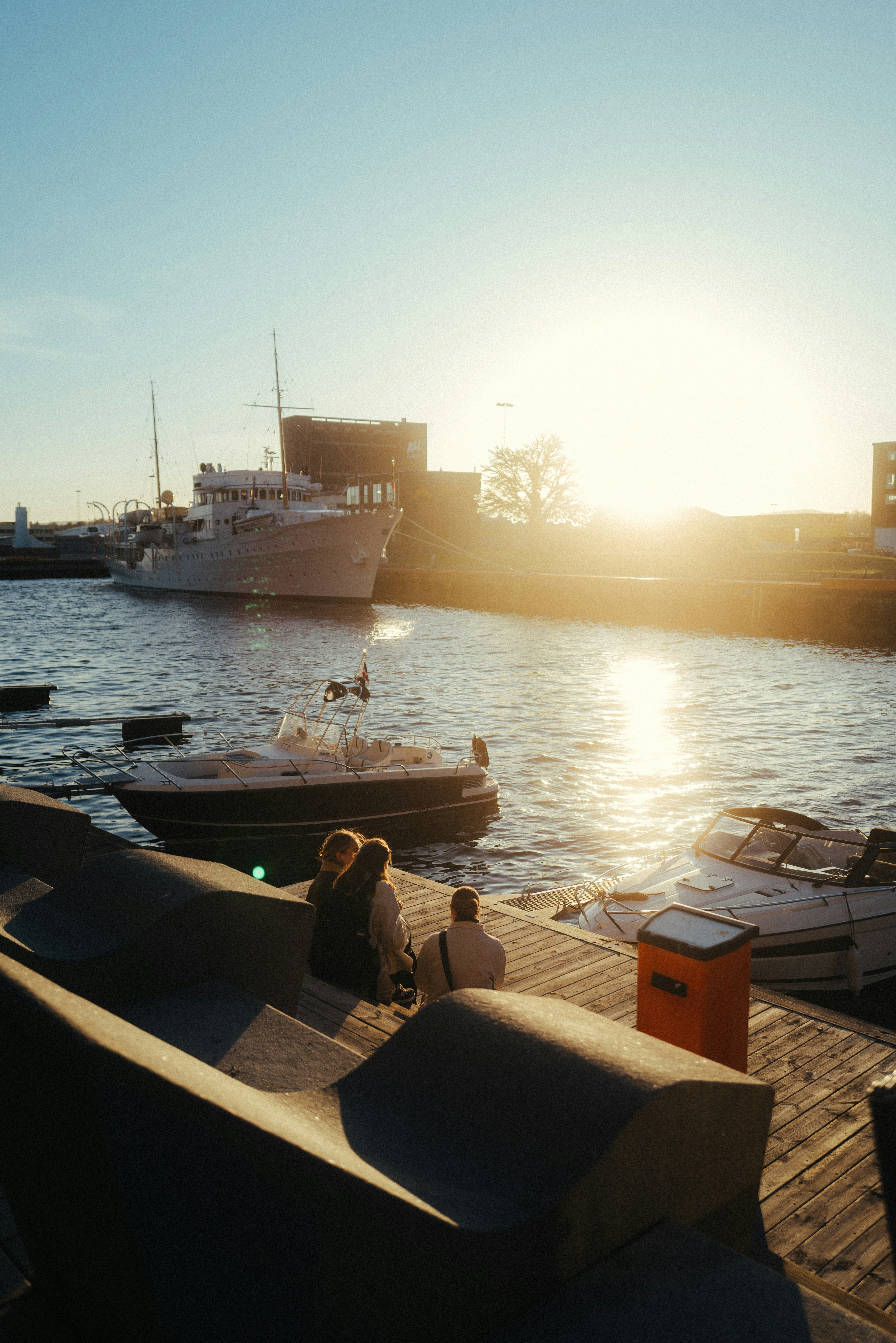 People watch sunset over boats in harbor.