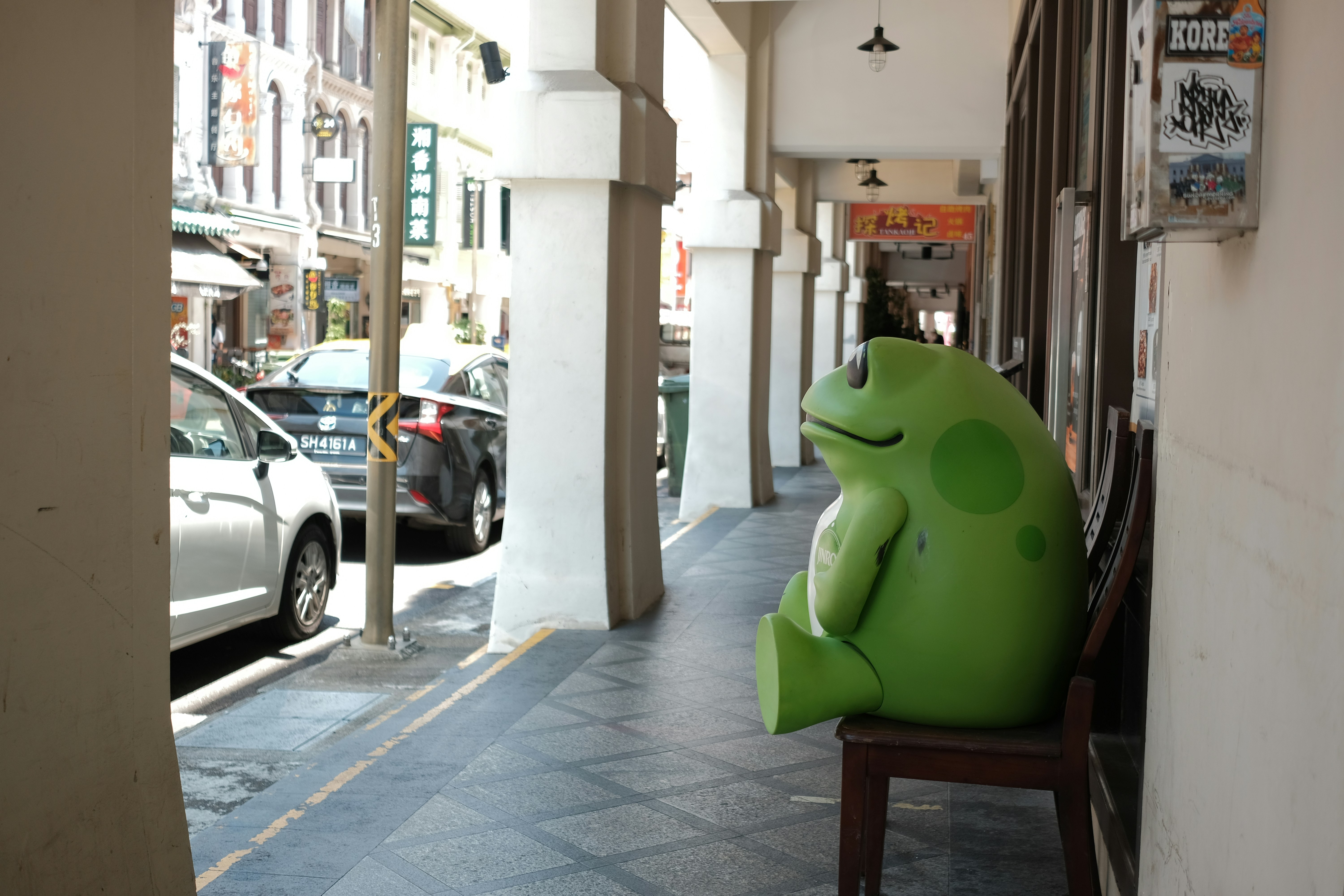 Urban Green Sentinel: A Plump Frog Statue Anchors the Shaded Arcade