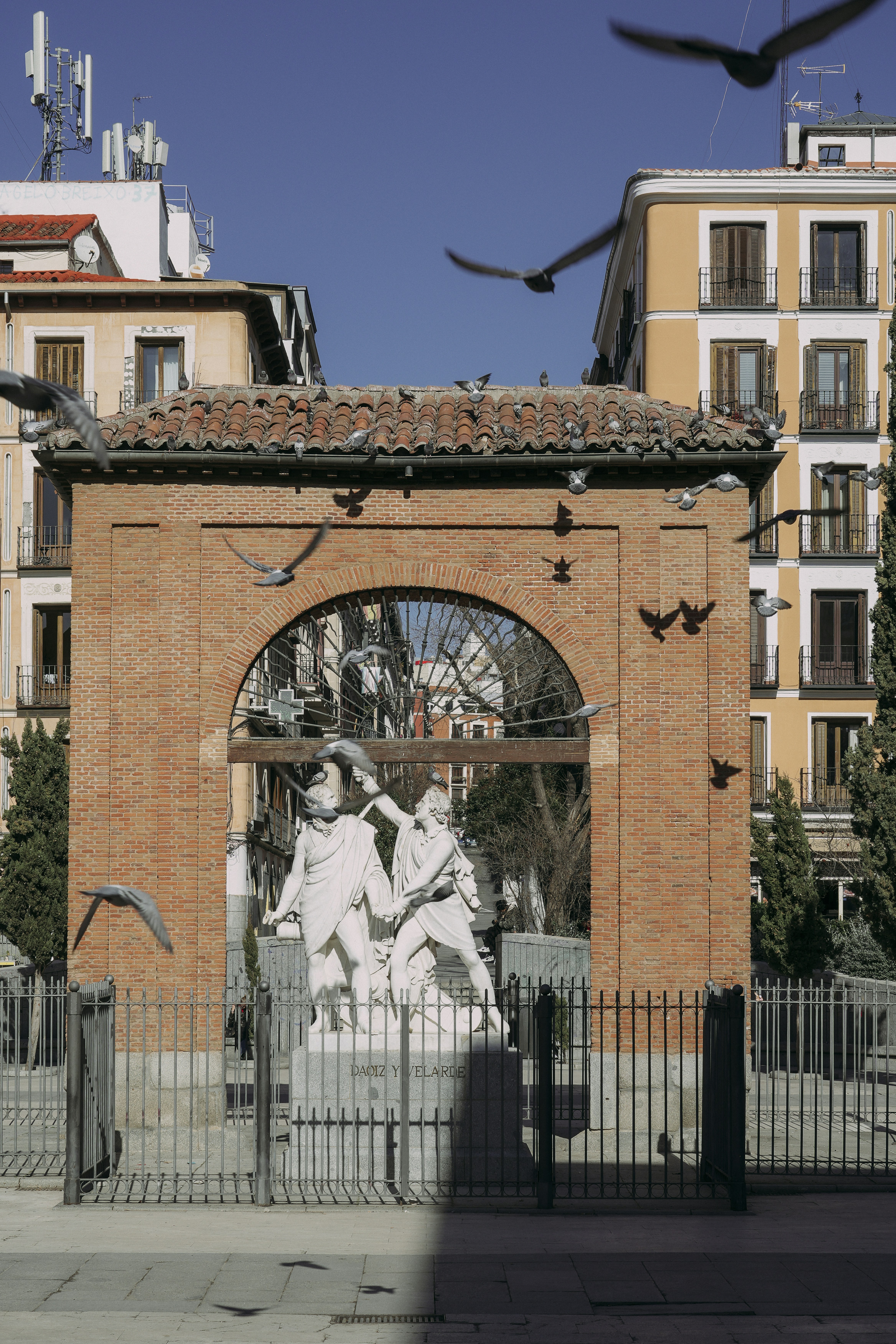 Birds fly around a brick structure with a statue. photo – Free Spain ...