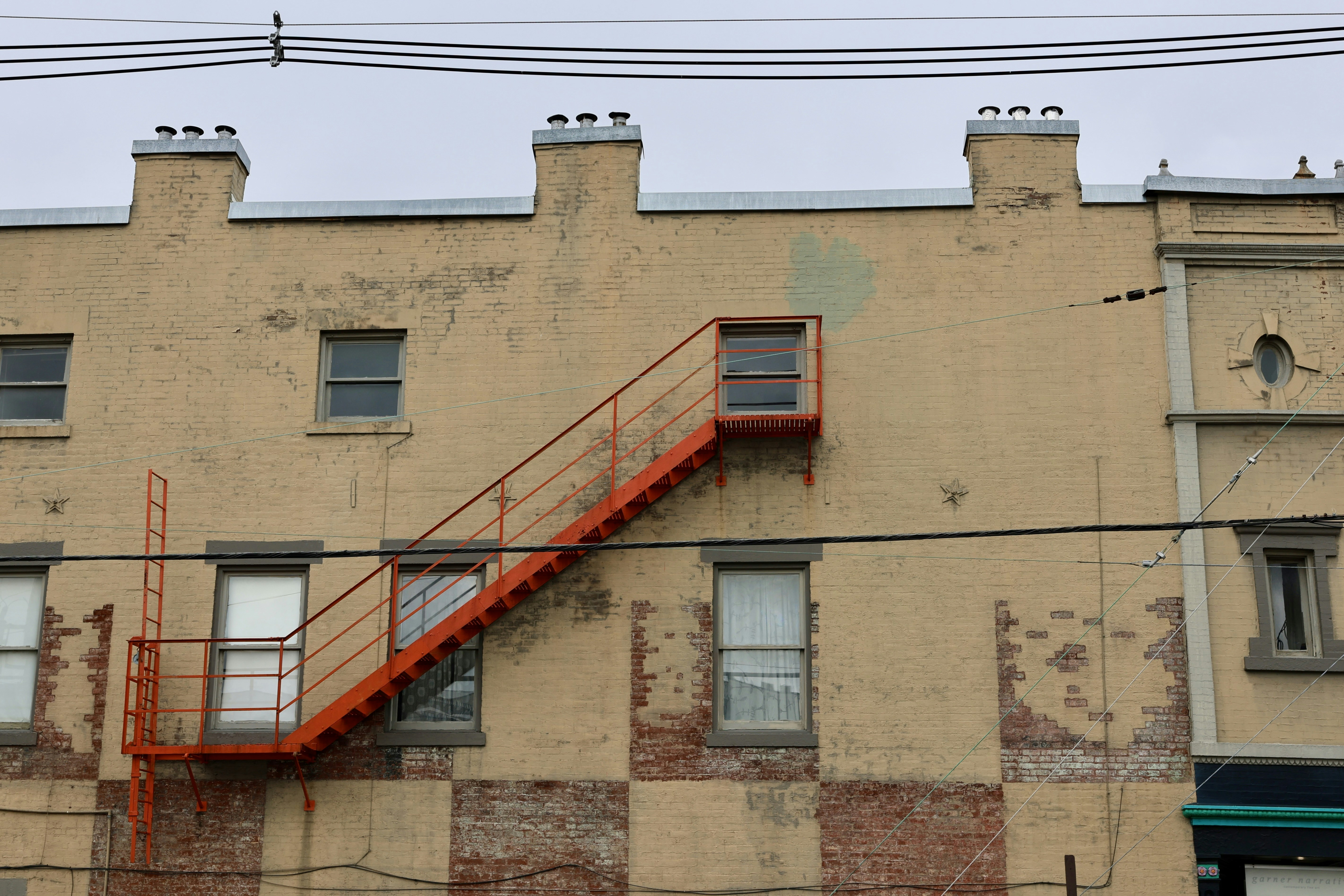Crimson Fire Escape Slices Across a Weathered Brick Facade