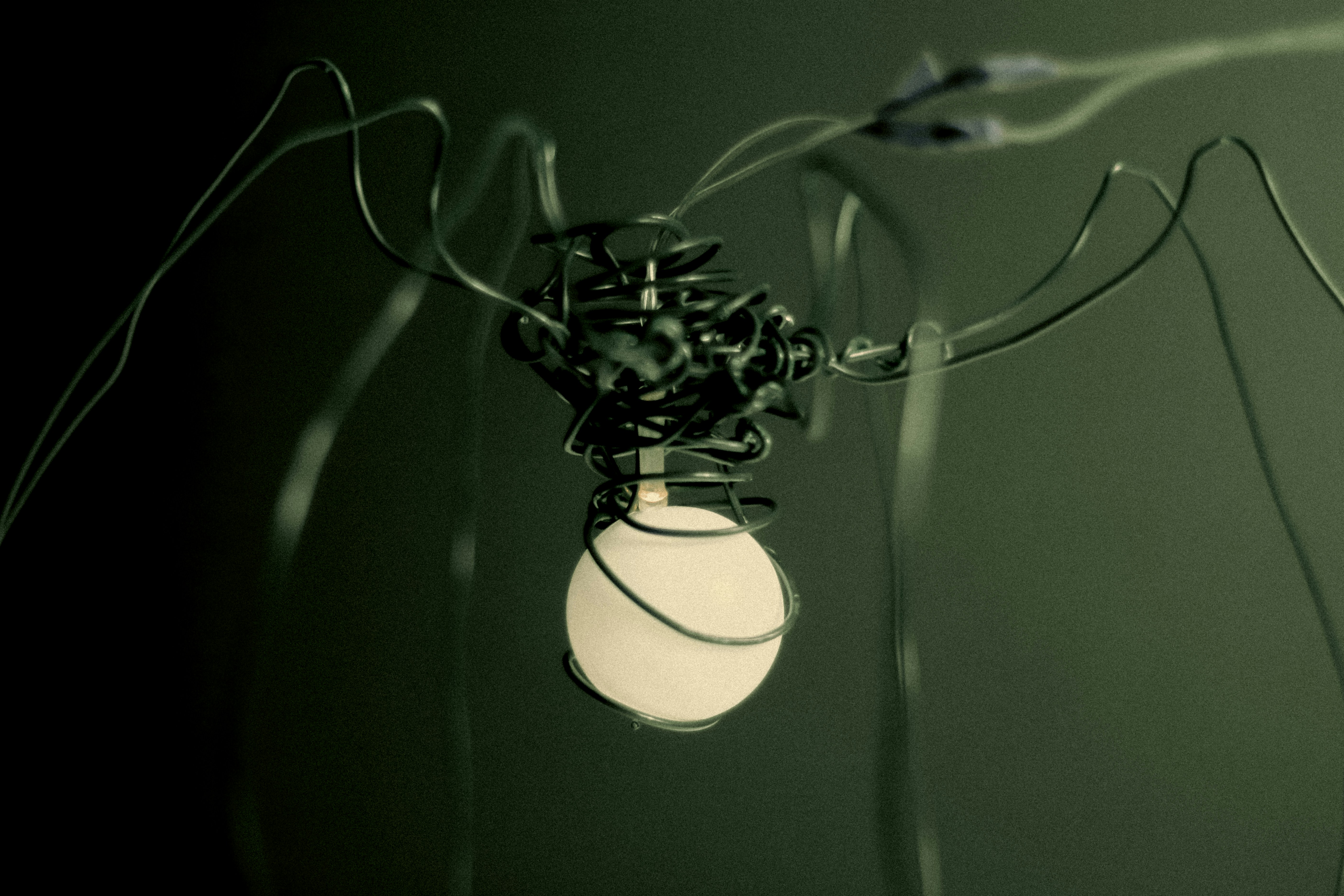 A whimsical sculpture of a light bulb ensnared in twisted black wires, creating an intriguing contrast against a muted background.
