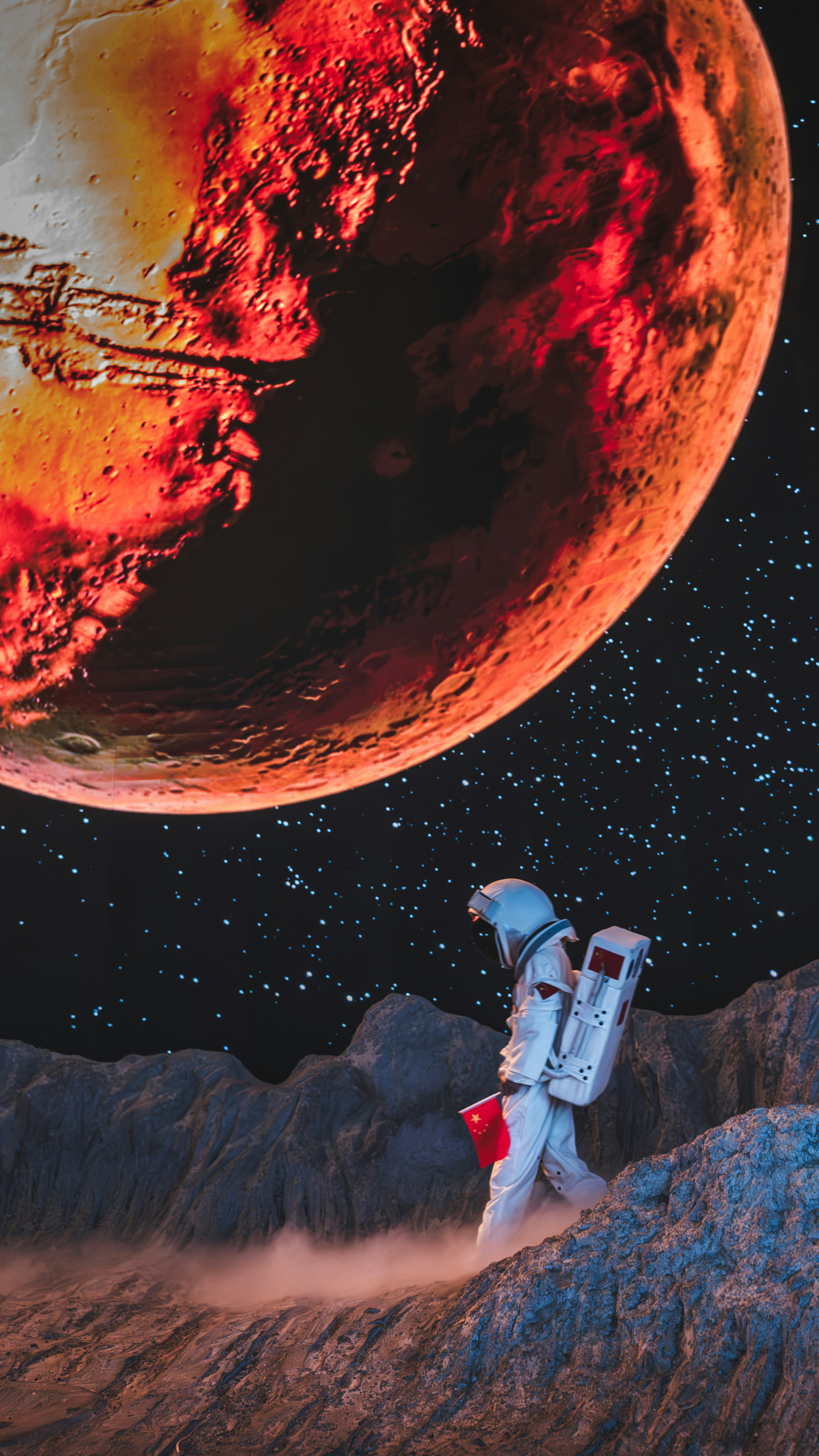 Astronaut on a rocky ridge holds a red flag as a giant crimson planet dominates the starry sky.