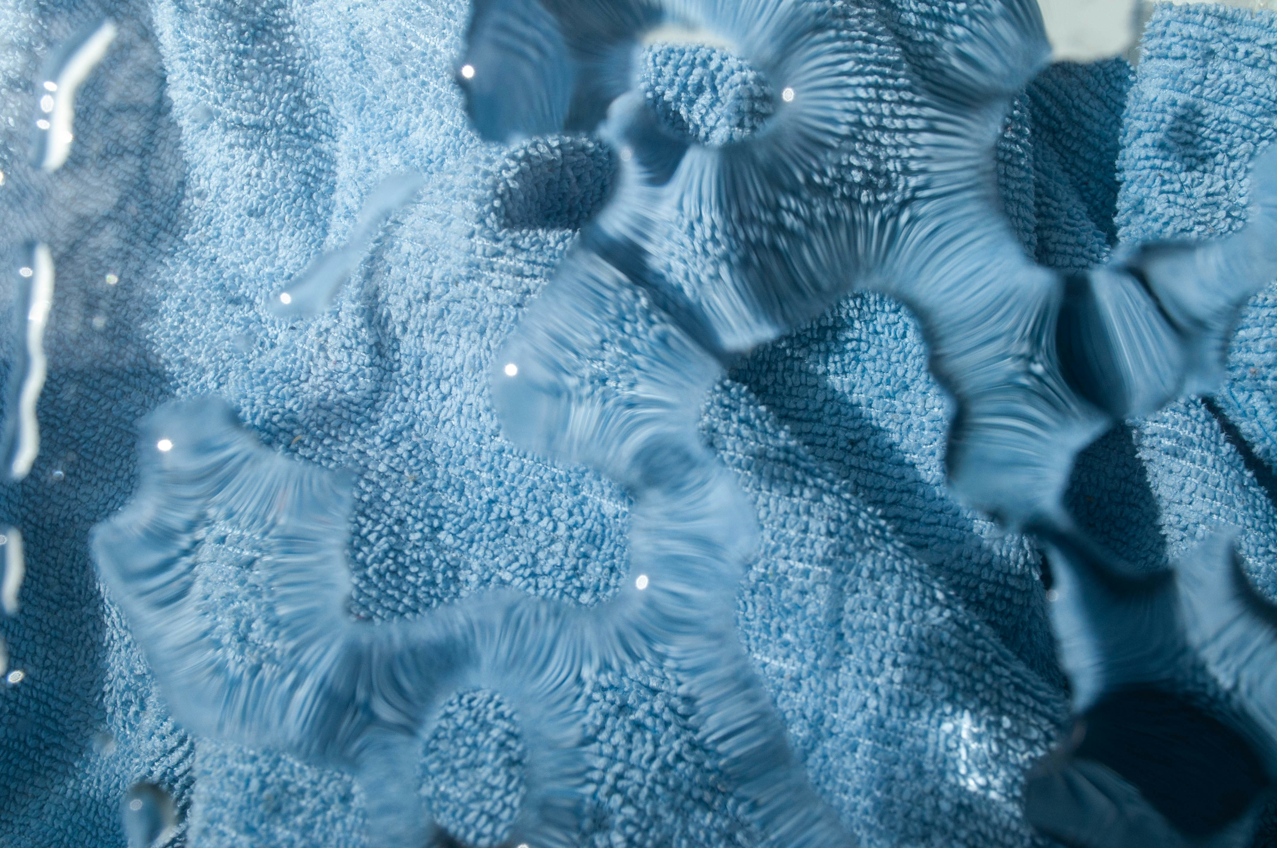 Water rippling over a textured blue towel, creating intricate patterns and reflections.