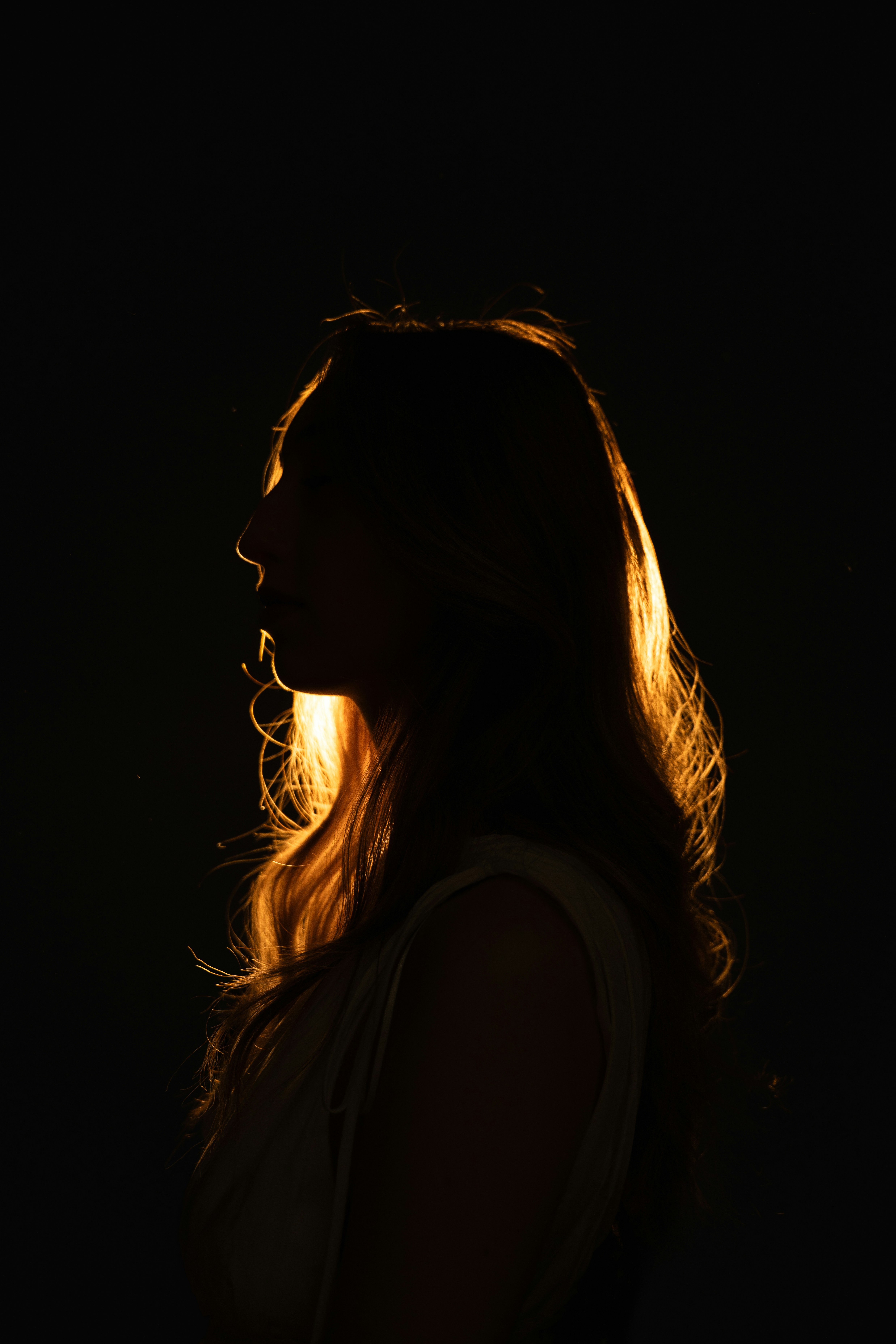 Silhouette of a woman against a dark background, illuminated by a warm glow from behind her hair.