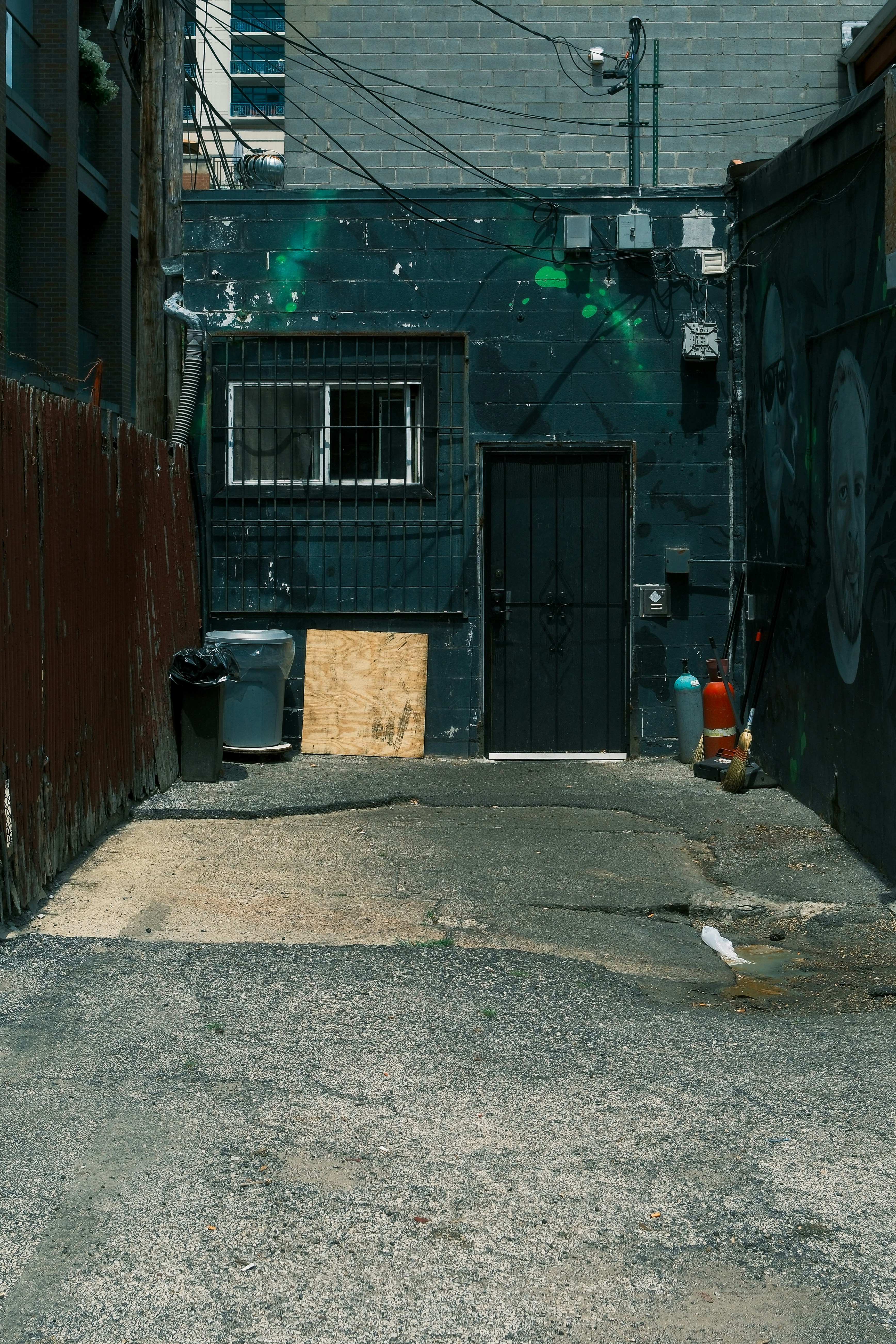 Dimly lit alleyway with a black door and graffiti-covered walls, showcasing urban decay and hidden stories.