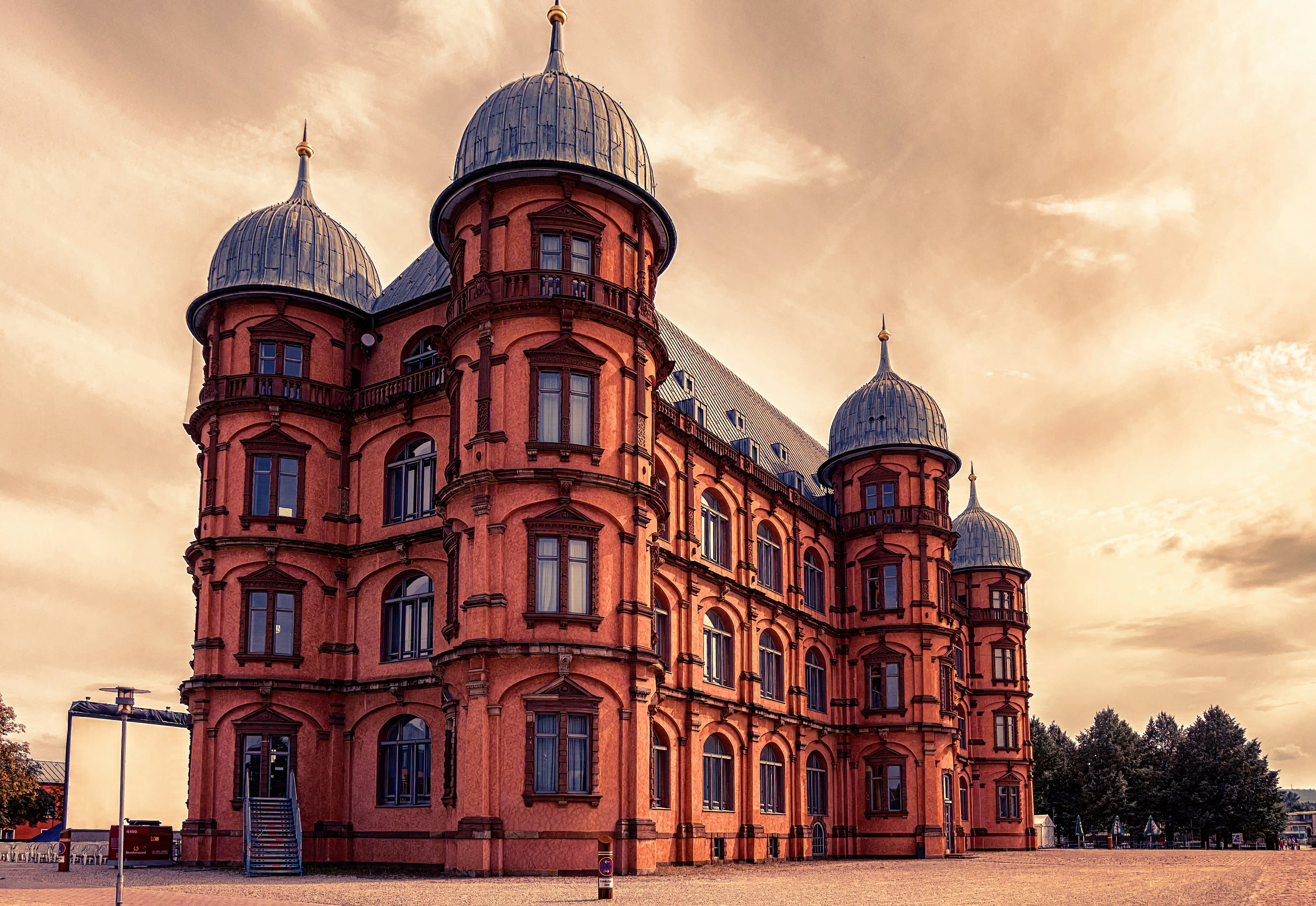 Intricate red building with domed roofs and ornate details, showcasing historic architecture against a dramatic sky.