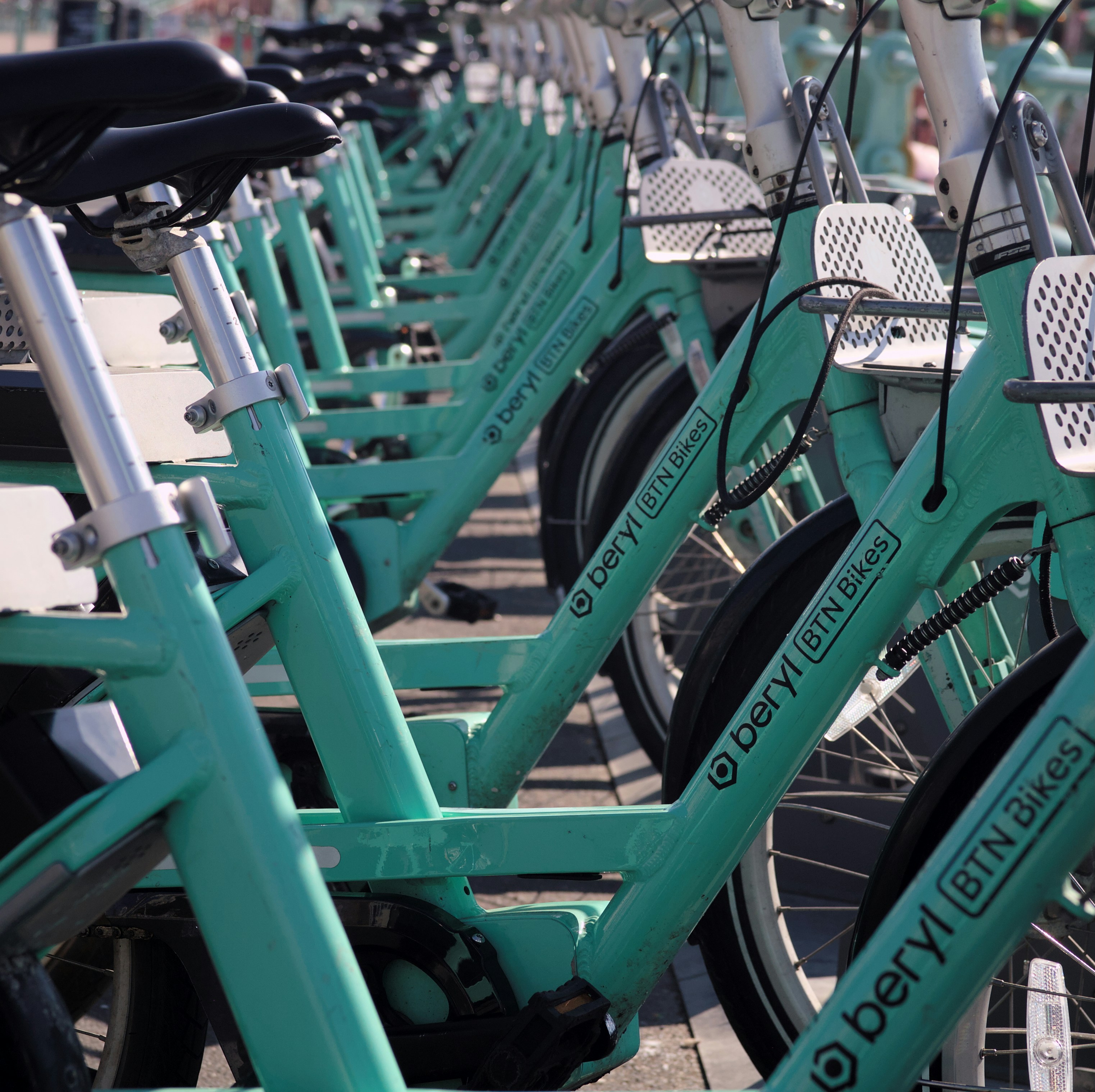 Row of turquoise bicycles parked in a bike-sharing station, showcasing their sleek design and branding. The scene reflects urban mobility and eco-friendly transportation.