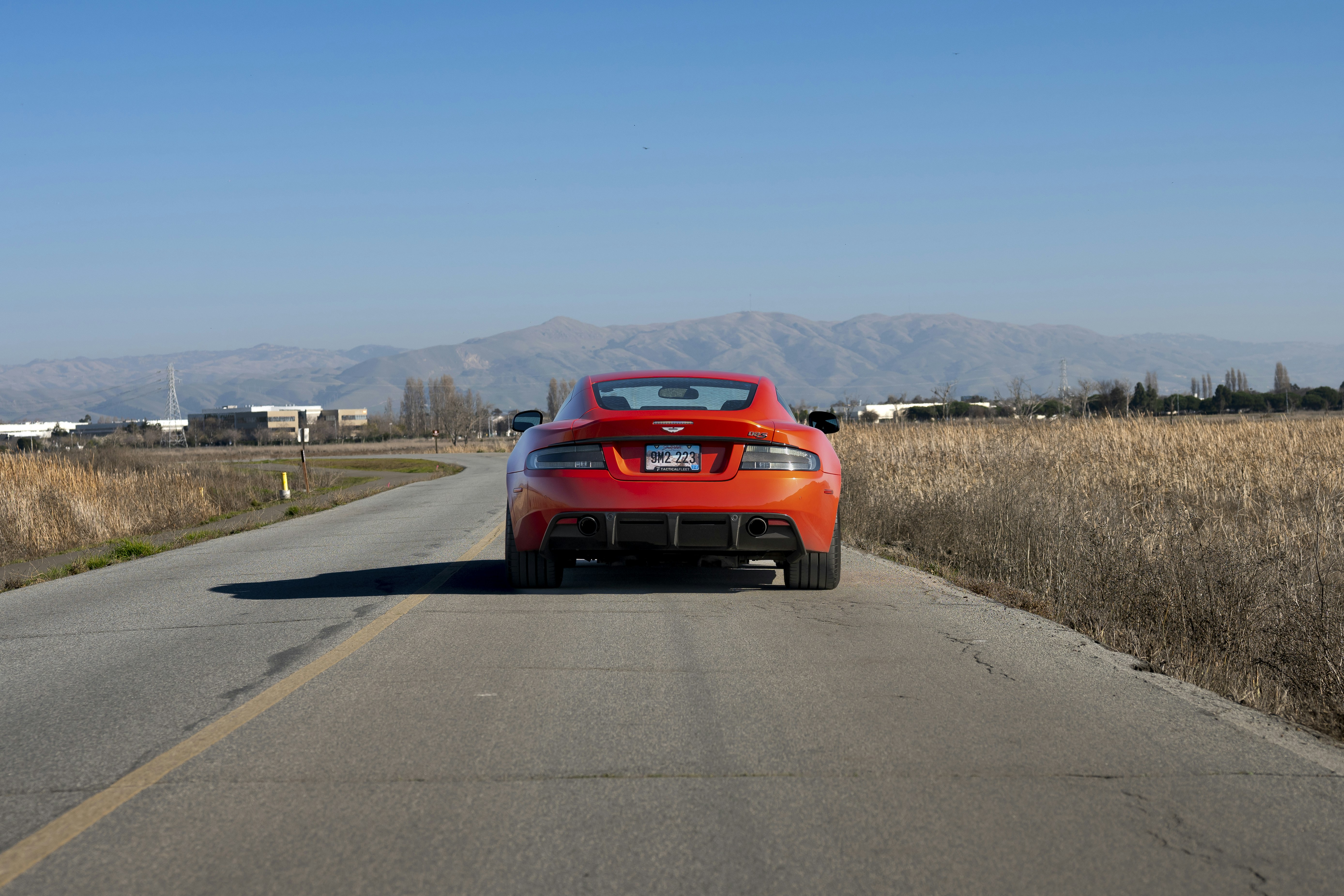 Red sports car on a sunlit rural road toward distant mountains