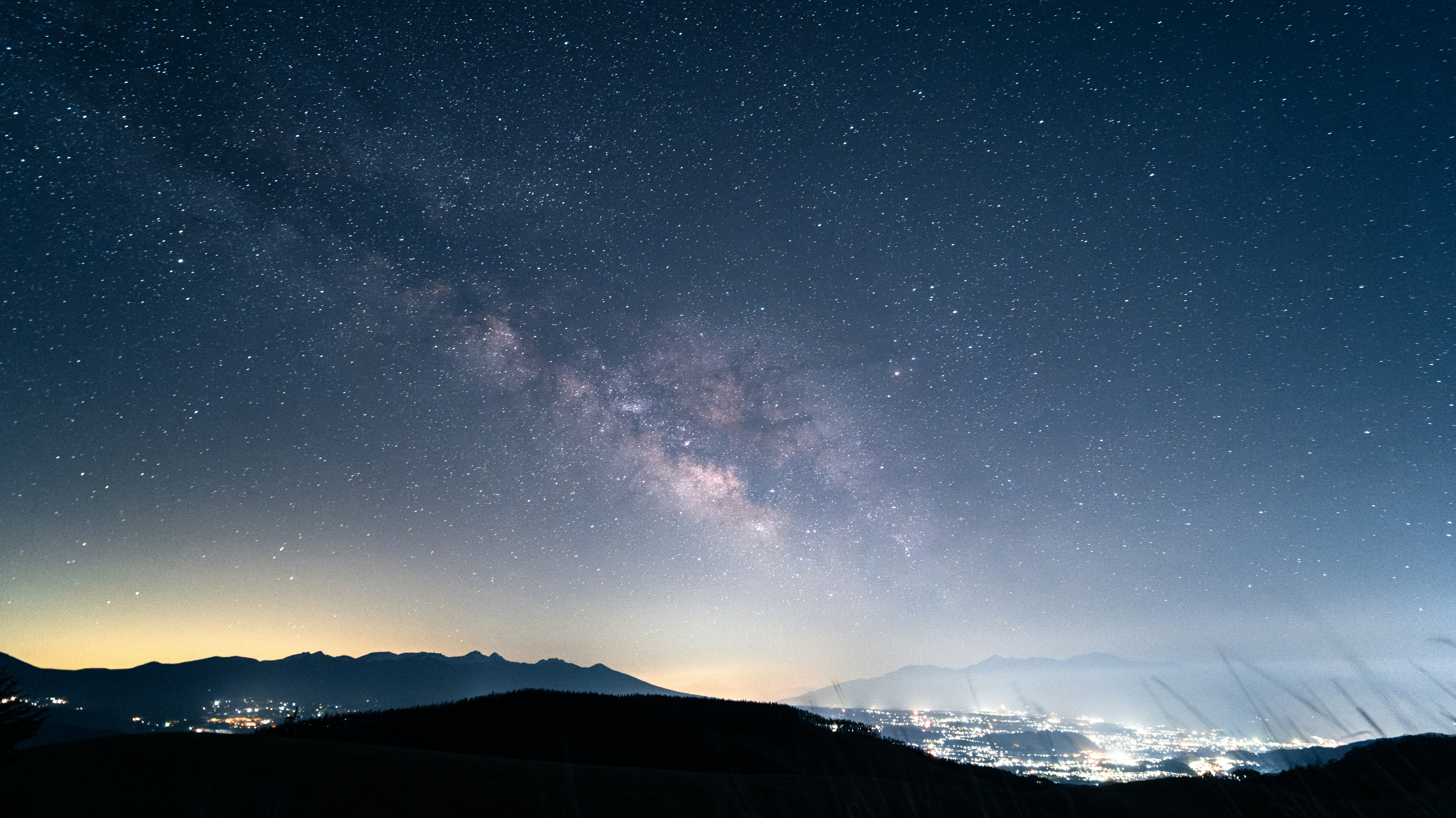 Milky way galaxy shines over distant land.