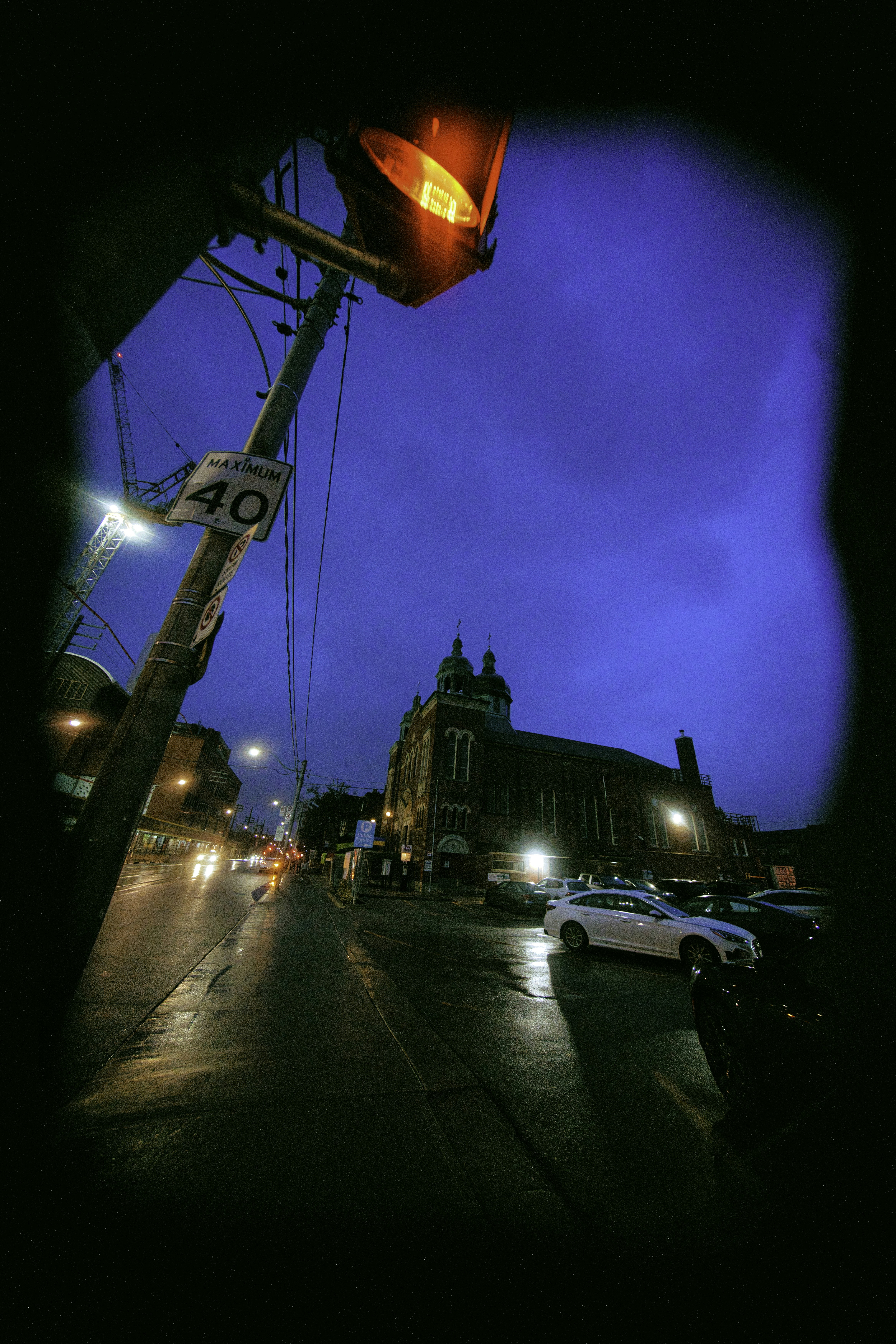 Traffic light glowing amber against a twilight sky, illuminating a wet city street with historic architecture in the background.
