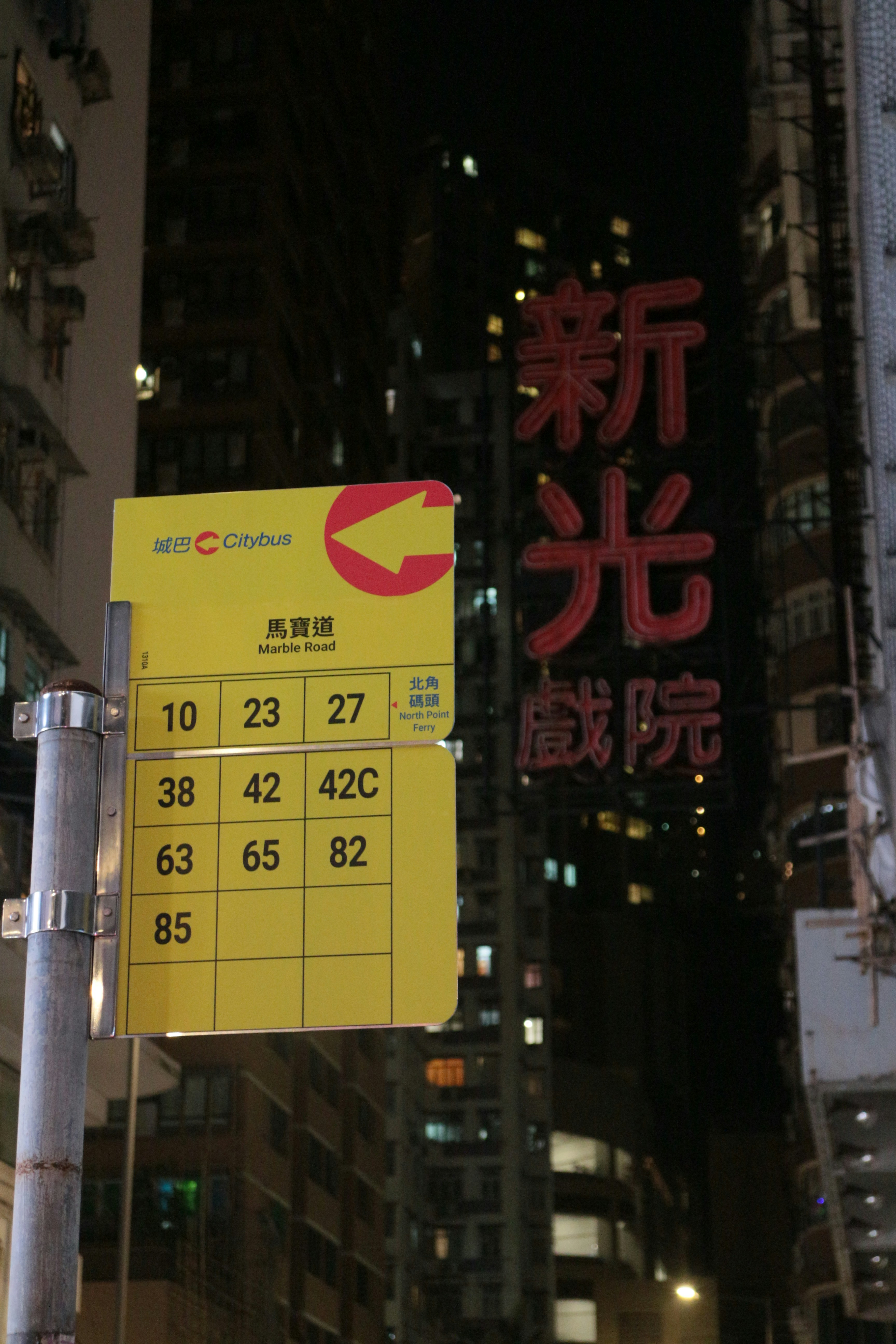 Citybus stop sign illuminated against a backdrop of neon signage in a bustling urban environment at night.