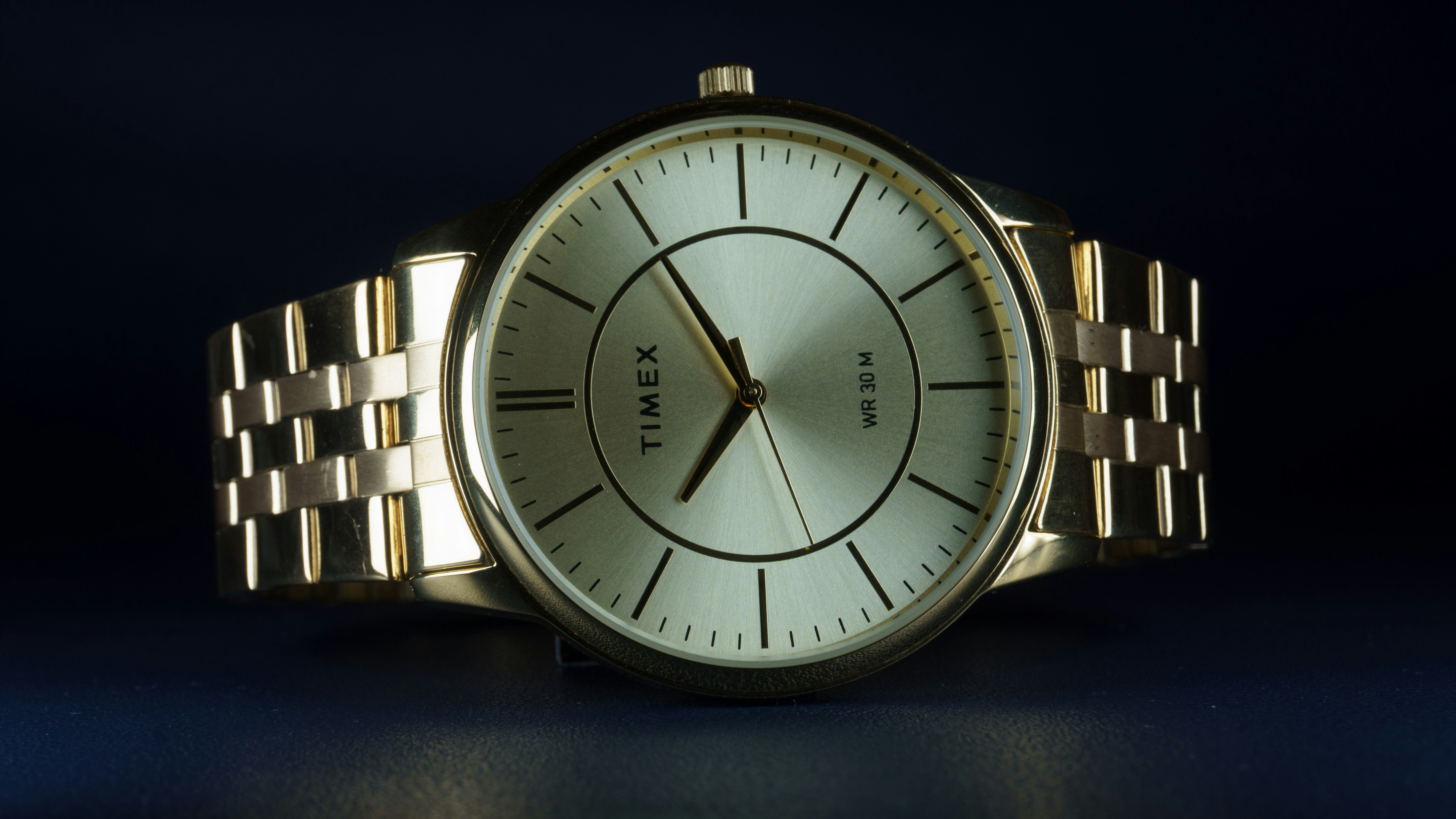 A gold timex wristwatch sits on a dark surface. photo – Free Watch ...