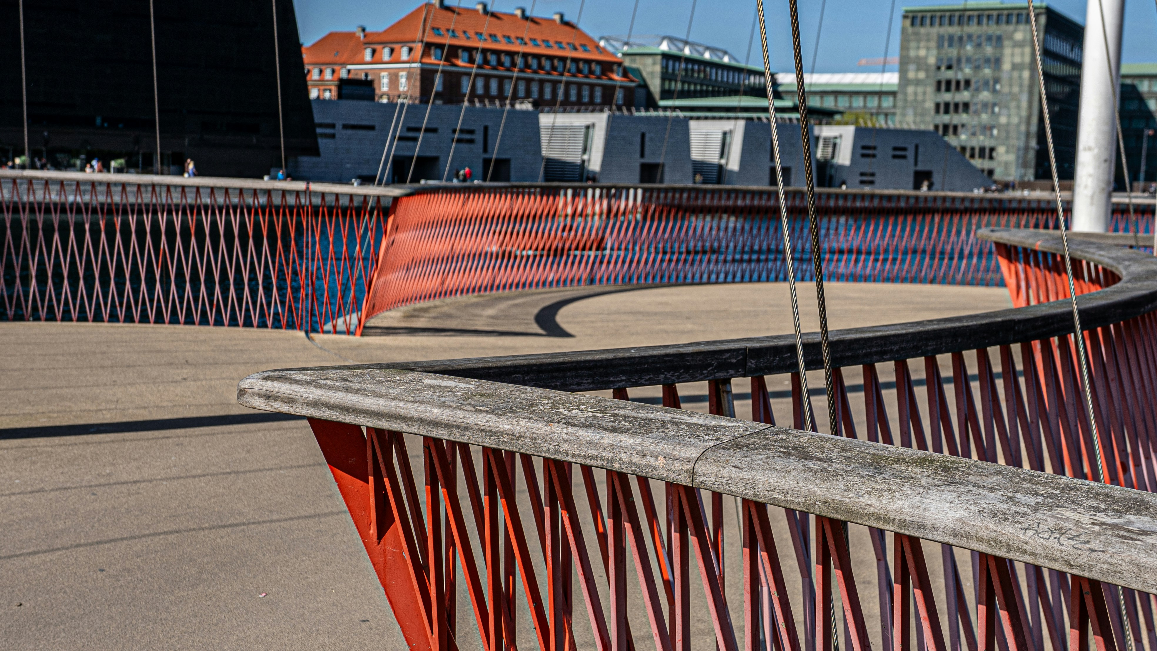 Crimson Lattice Rails Lead the Eye Across a Modern City Bridge