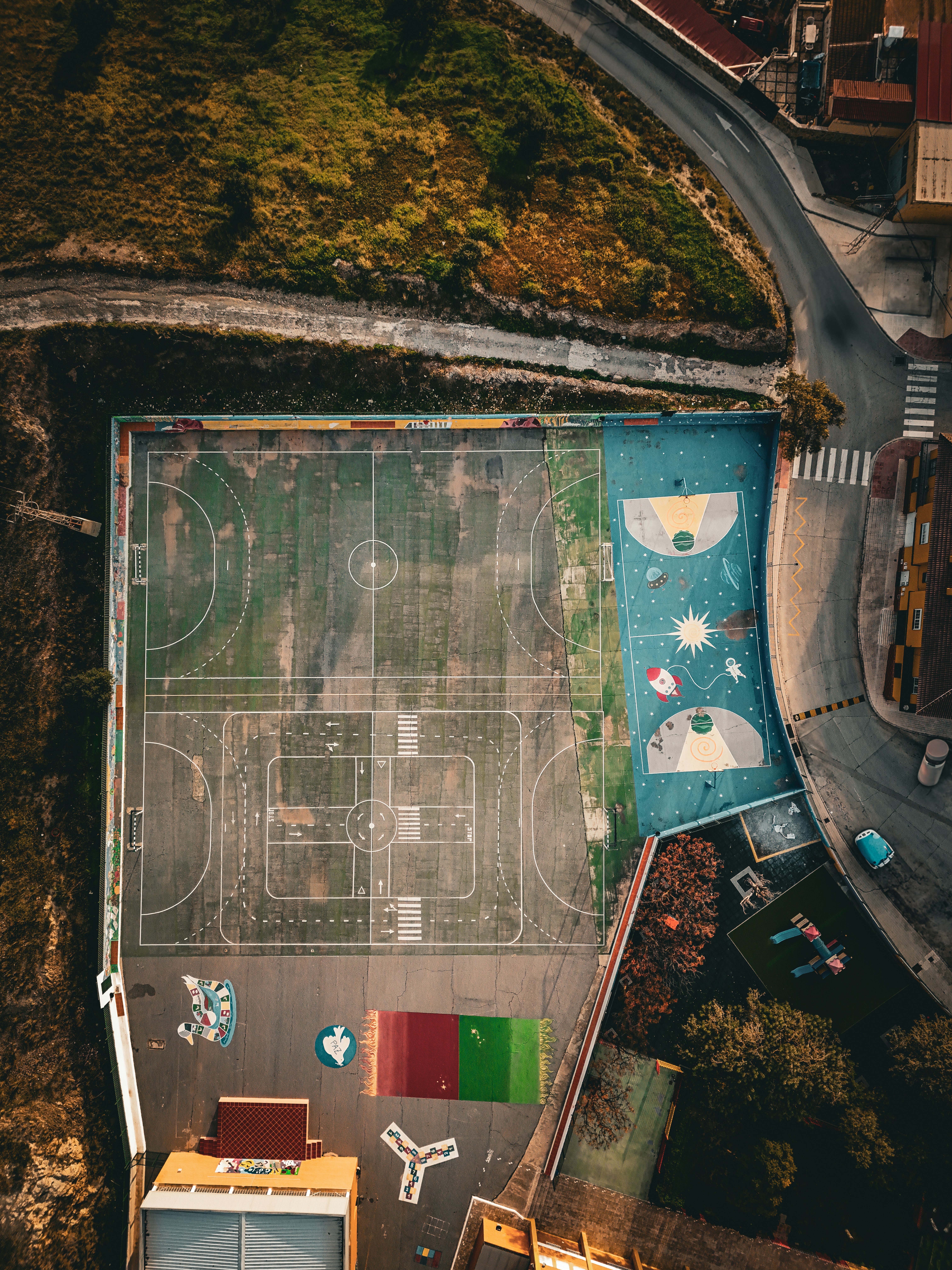 Vibrant basketball court viewed from above, showcasing colorful markings and surroundings. The layout highlights areas for play and creativity.