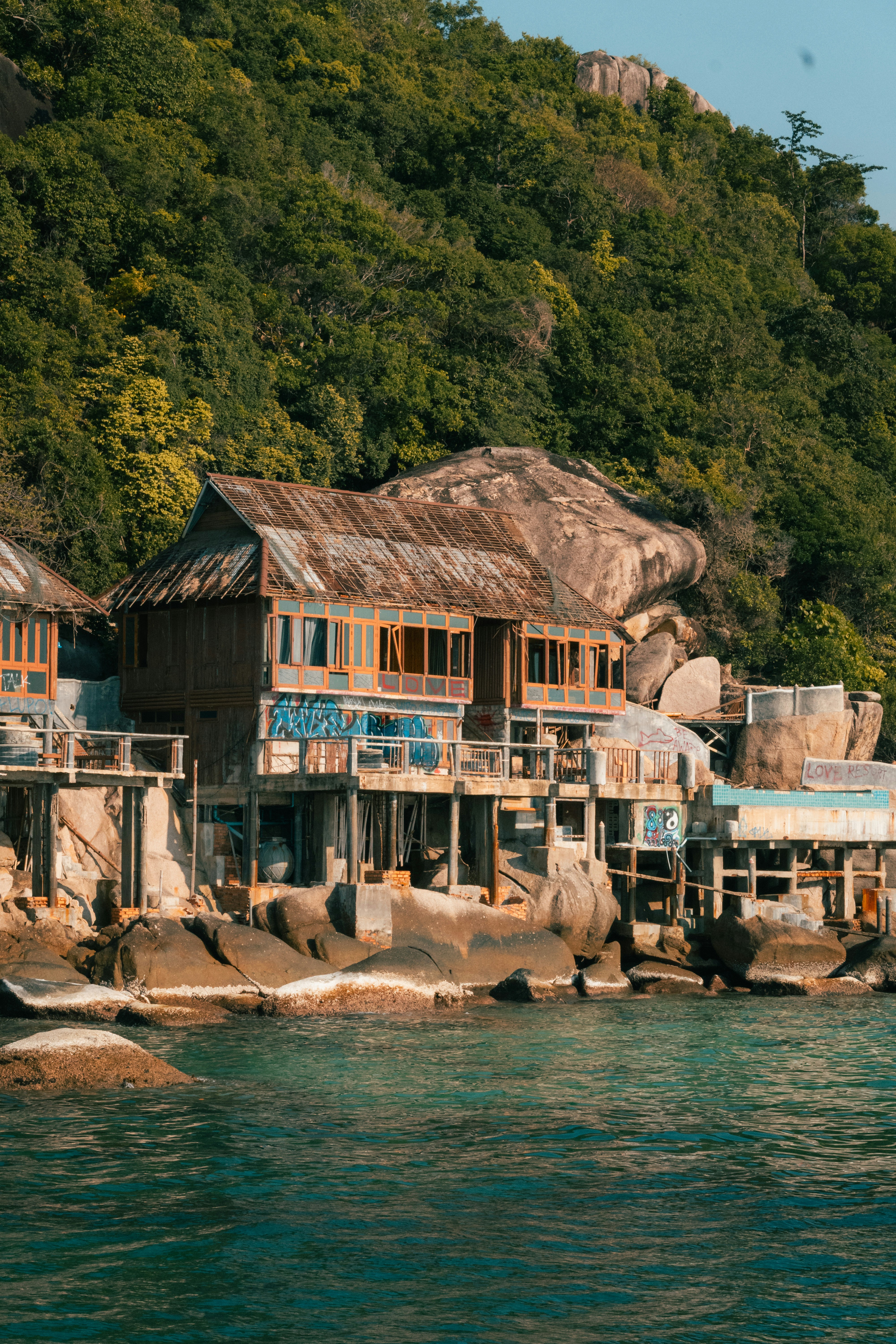 Weathered Waterfront Cabins Clinging to a Rocky Shore Beneath a Forested Slope