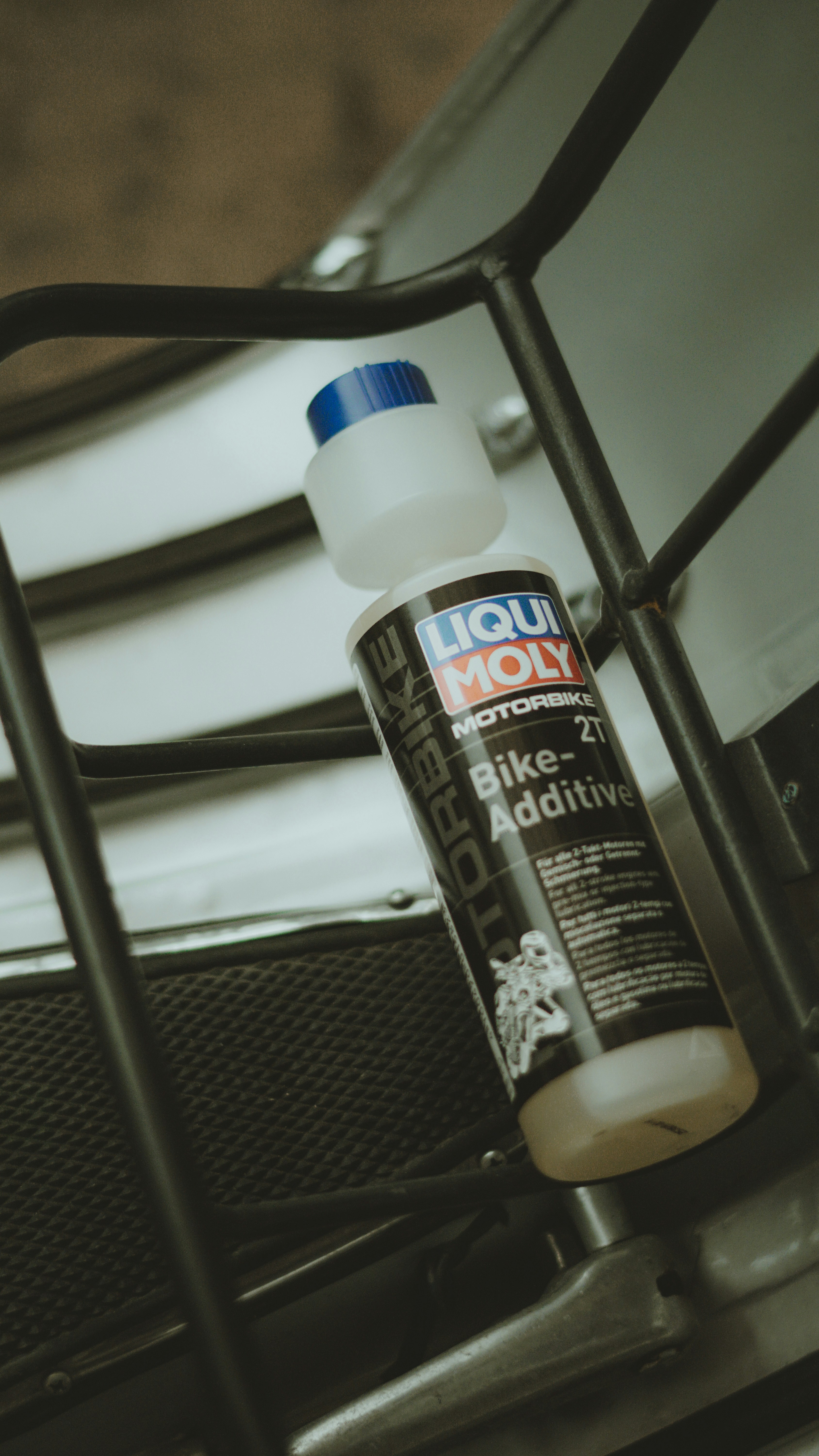 Close-up of a LIQUI MOLY motorbike additive bottle bearing the logo, set within a metal motorcycle frame.