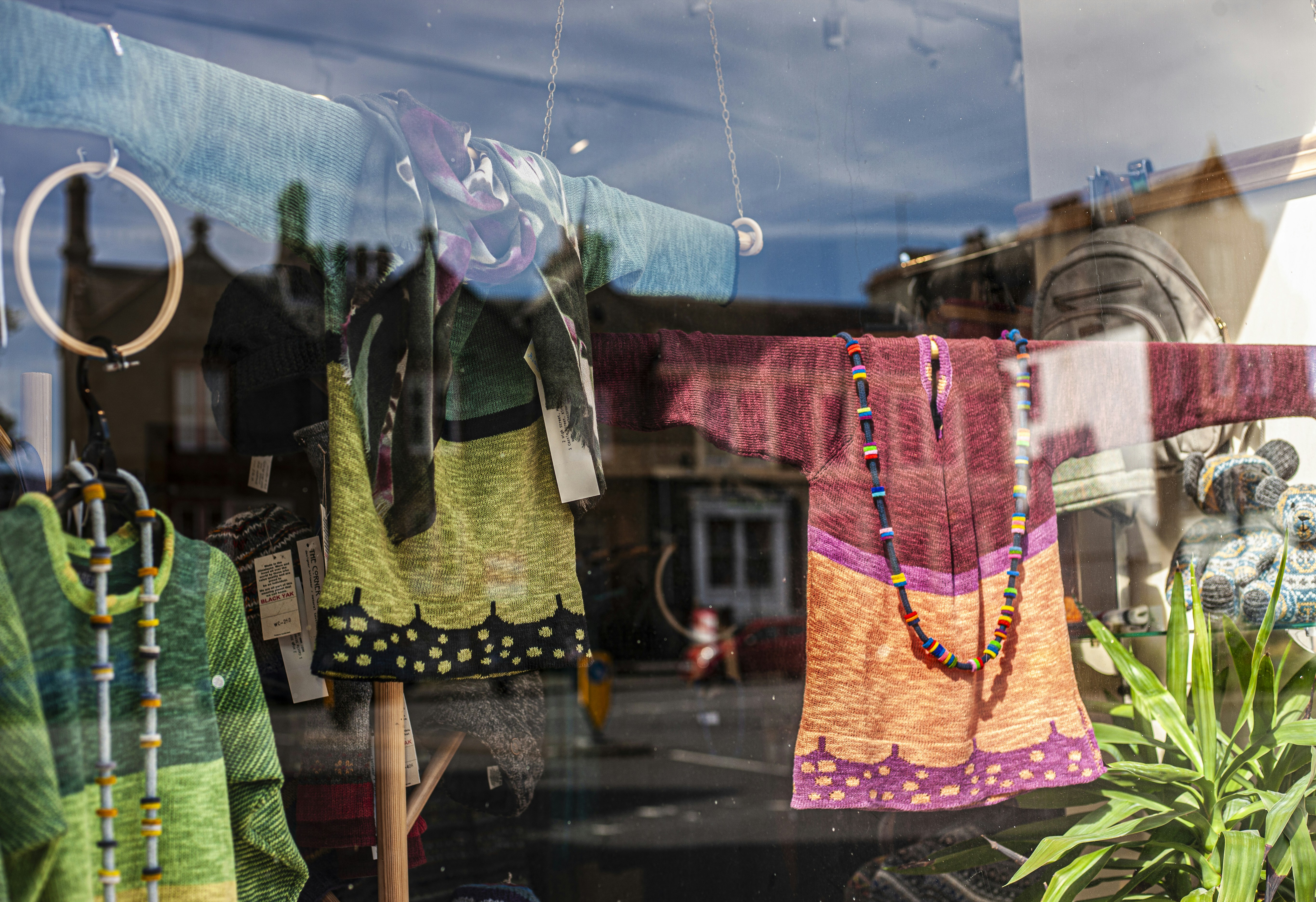 Colorful textiles in a storefront window reflecting a sunlit street