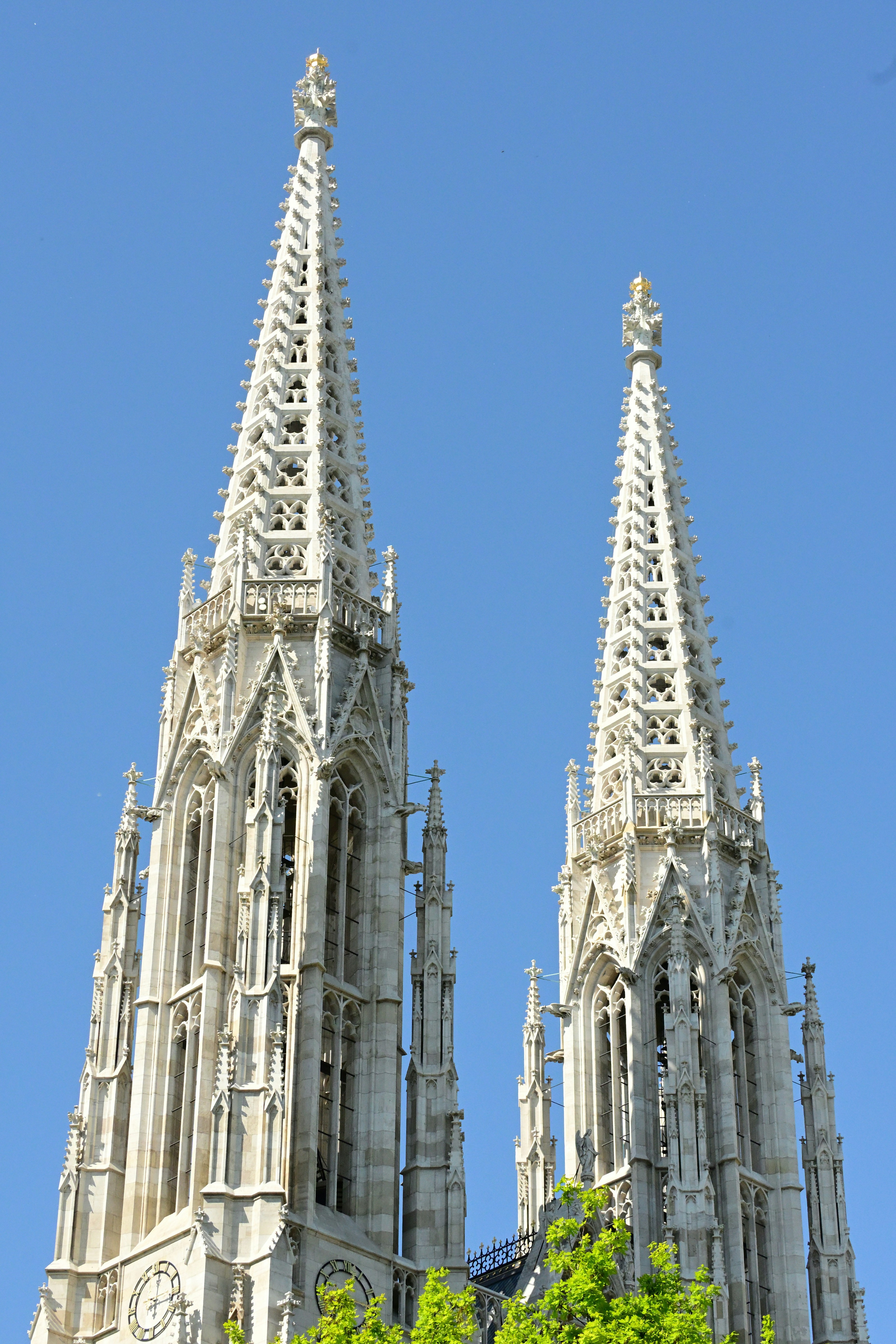 Intricate gothic spires of a cathedral rise against a clear blue sky, showcasing detailed stonework and architectural elegance.