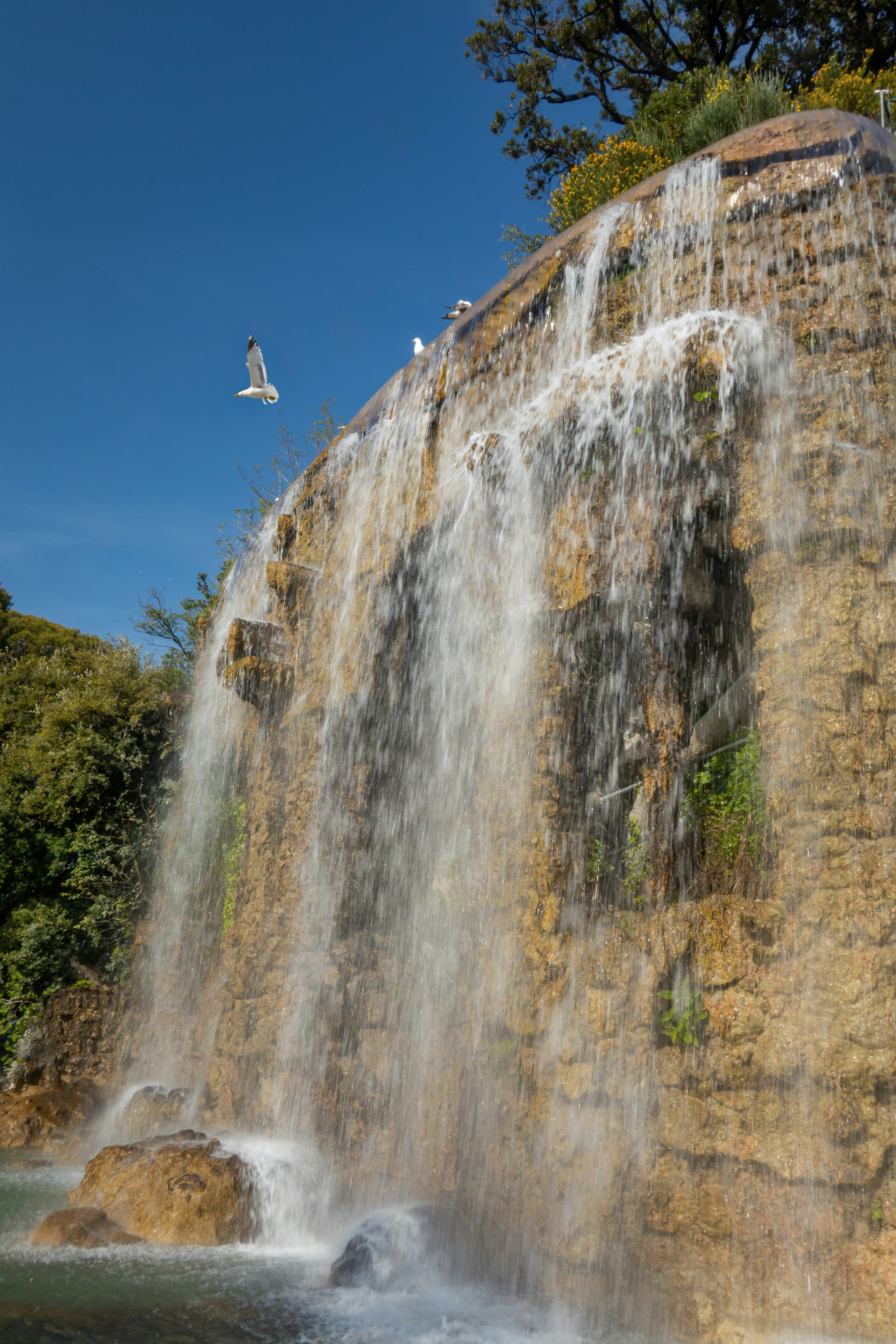 Sunlit Curtain on a Cliff: Waterfall Spray Beneath a Blue Sky