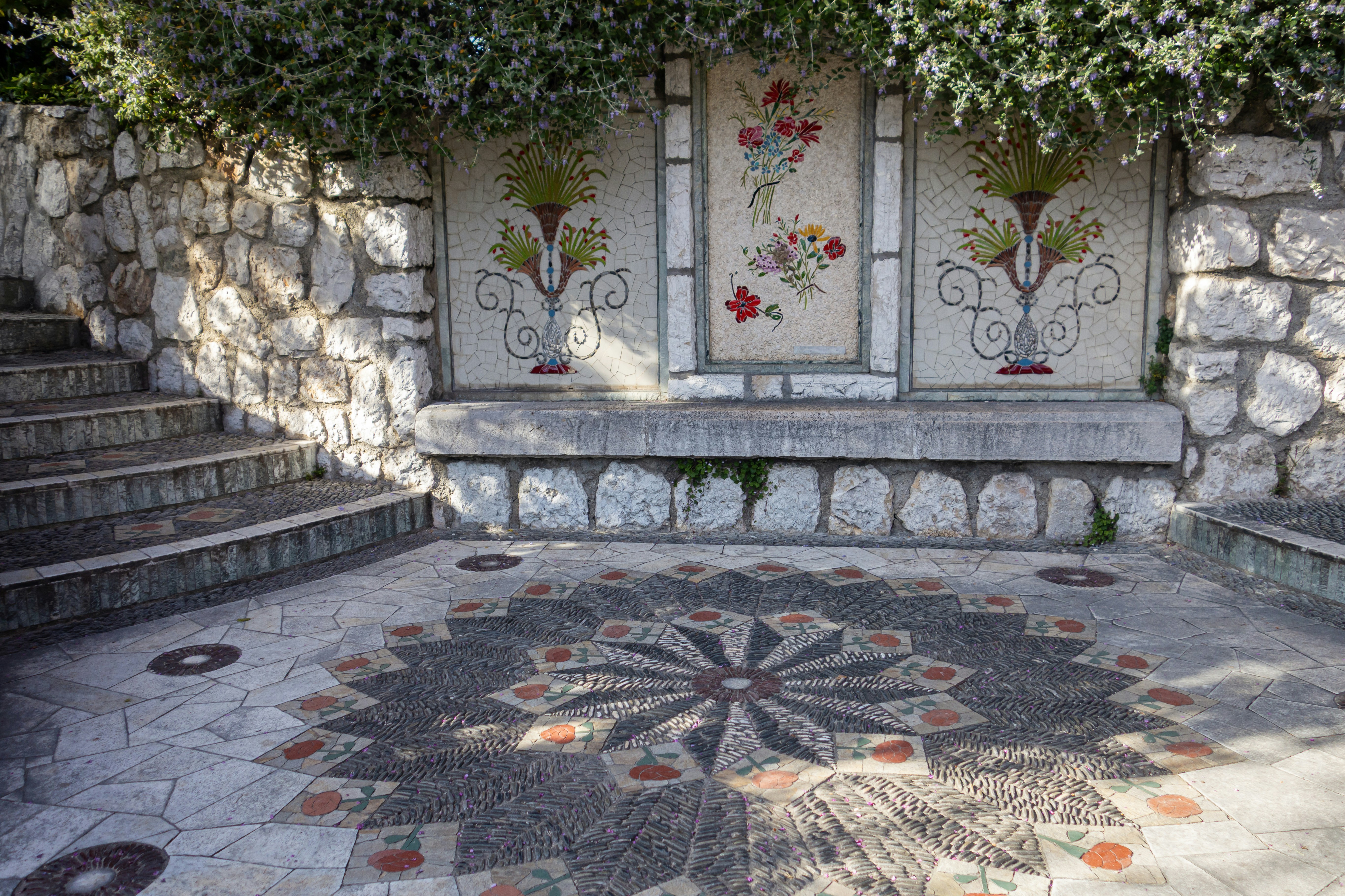 Circular mosaic in a sunlit courtyard with stone wall and garden art