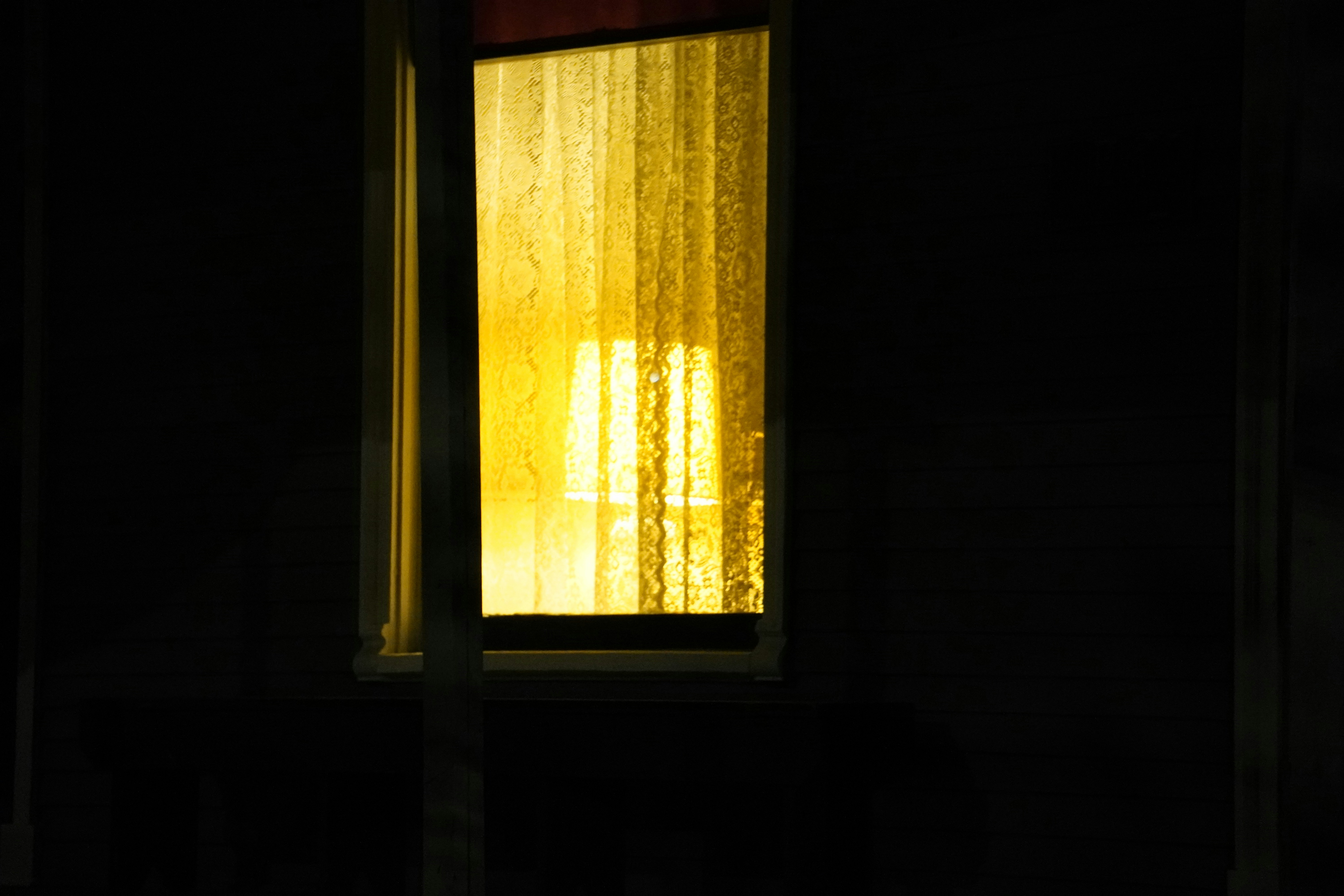 gothic victorian lamp in window | Glowing light shines through a window in the dark.