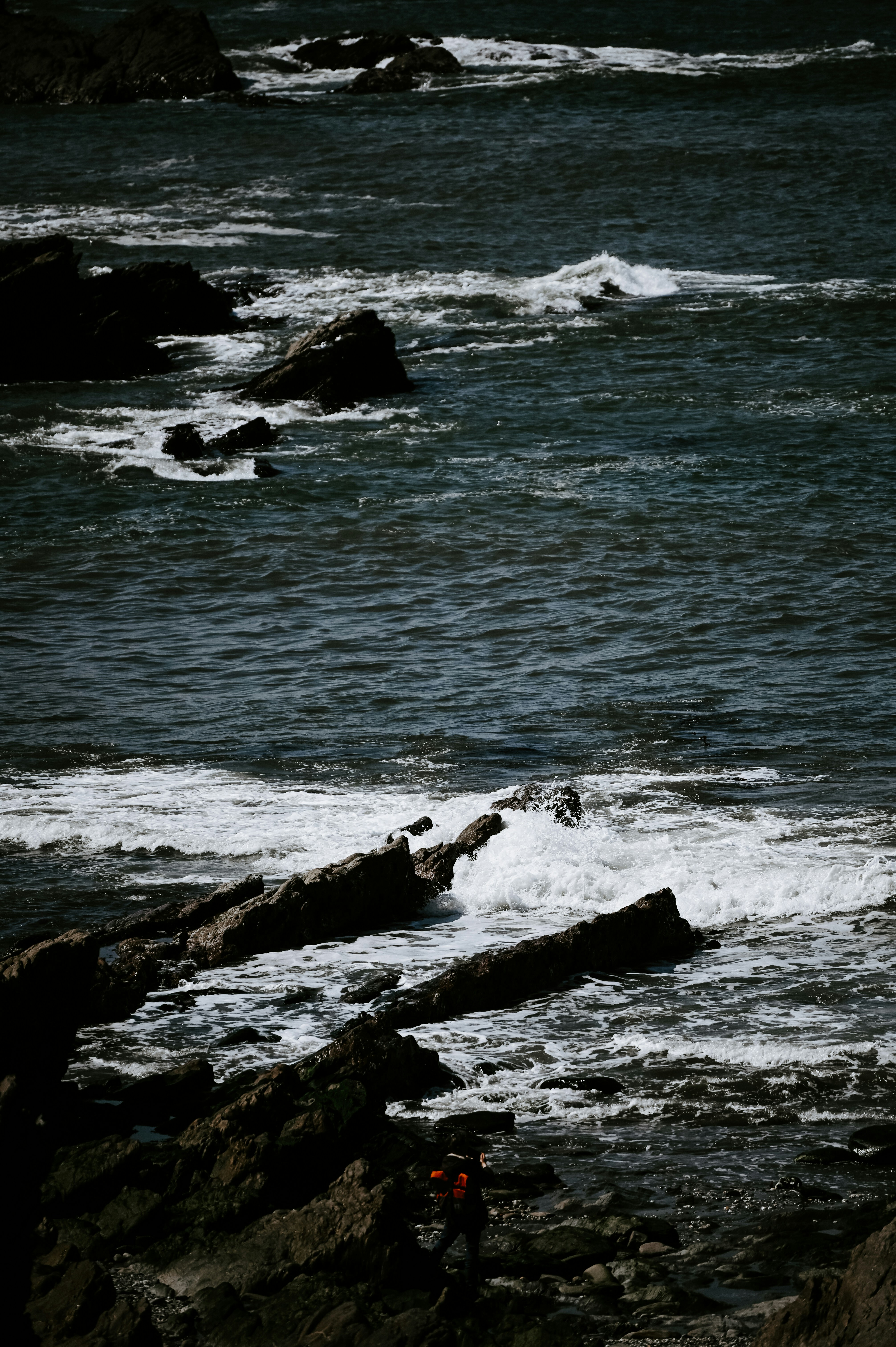 Rocky shoreline with distant surfer braving the surf