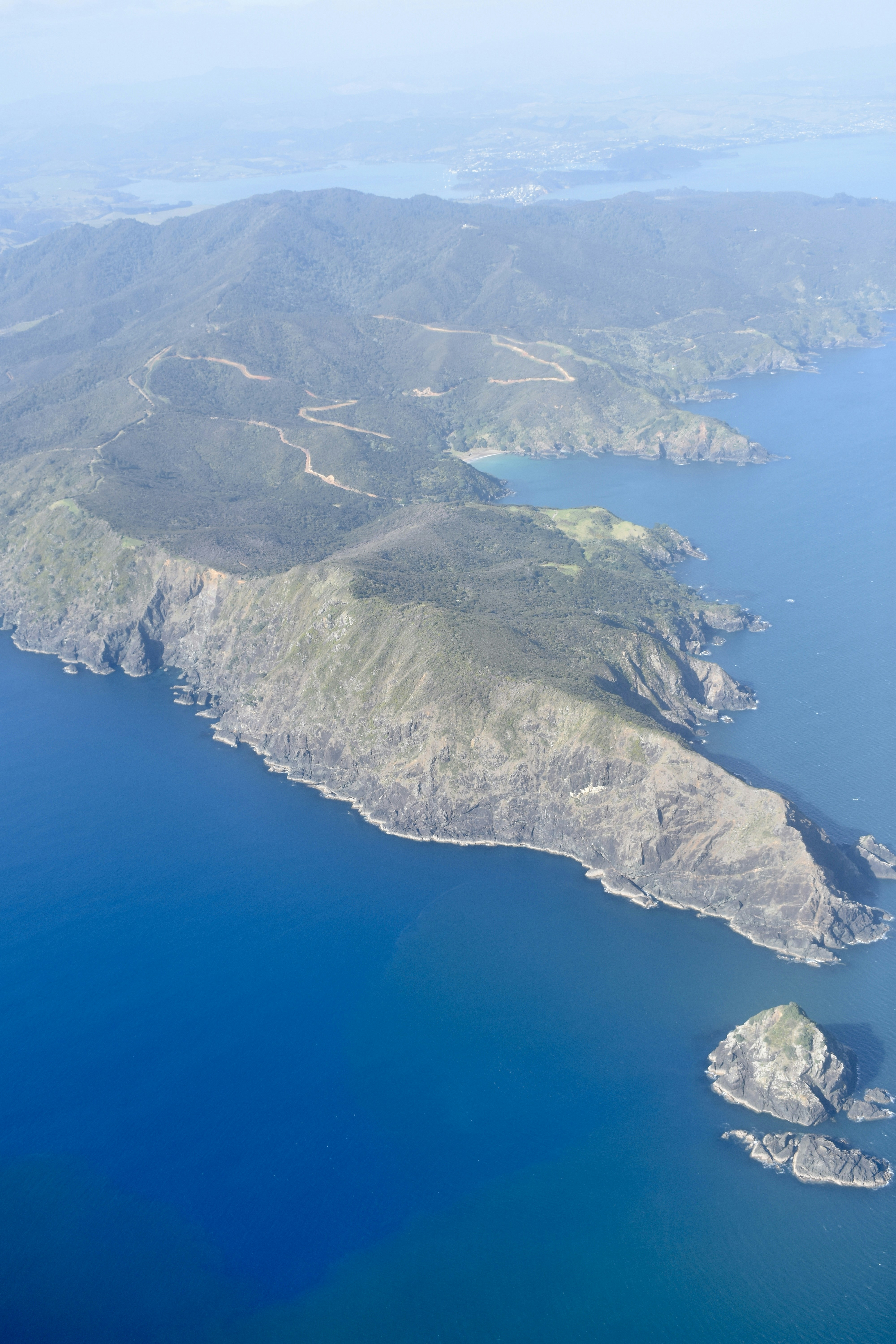 Aerial perspective showcasing a rugged coastline with lush greenery and deep blue waters, highlighting the natural beauty of the landscape.