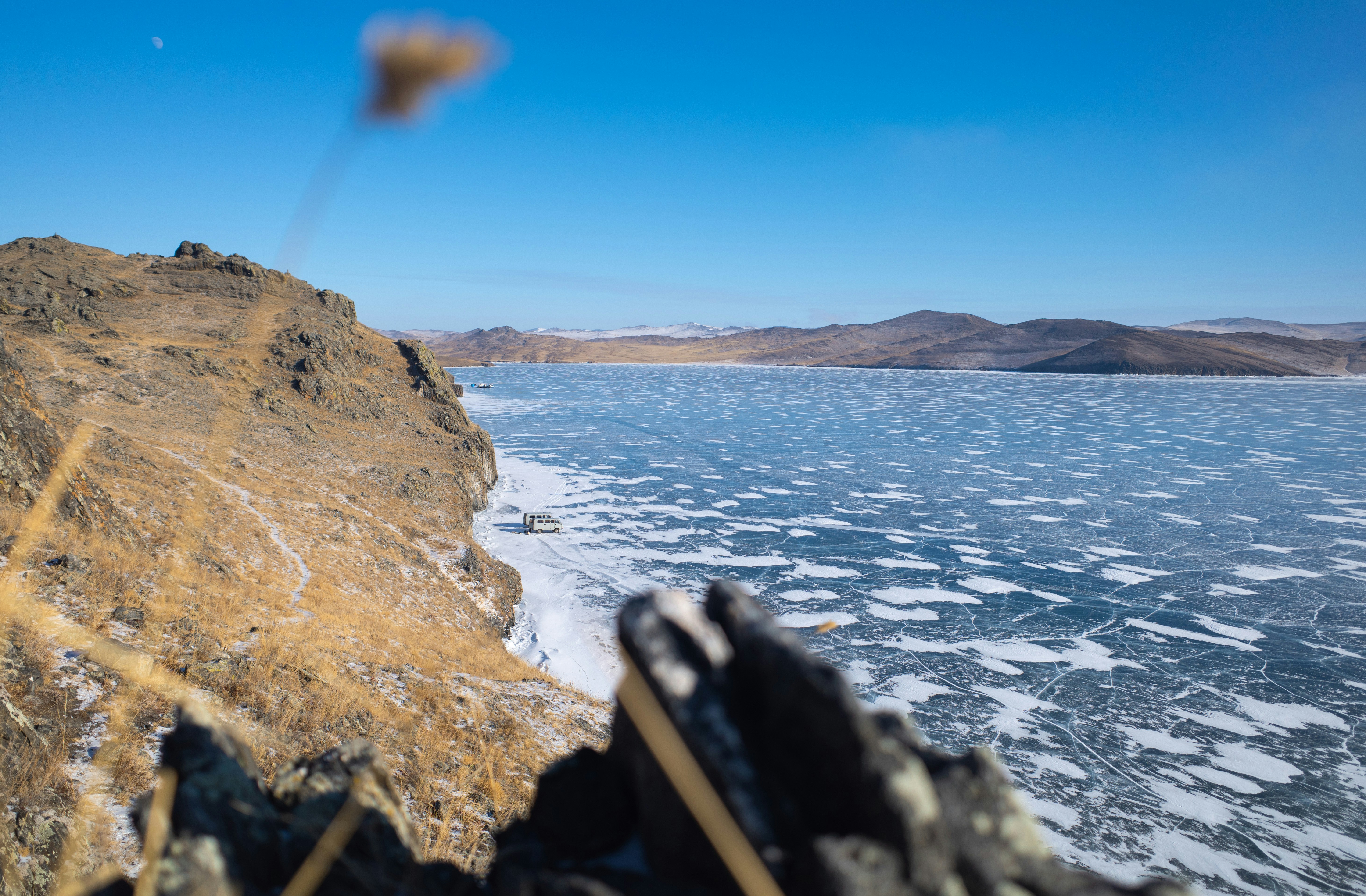 Edge of Ice and Rock: A sunlit shoreline framing a frozen lake under a clear blue sky