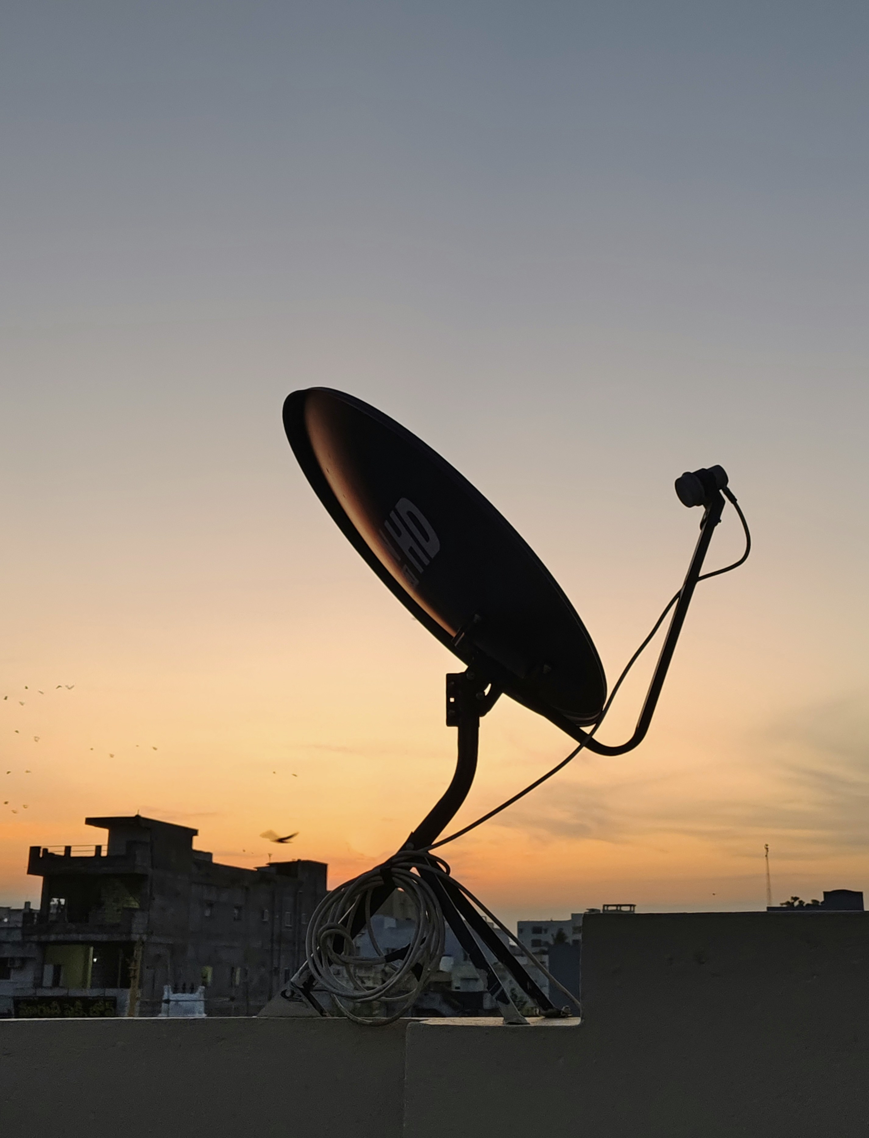 Dusk Relay: Rooftop Satellite Dish Silhouetted Against a City Sunset