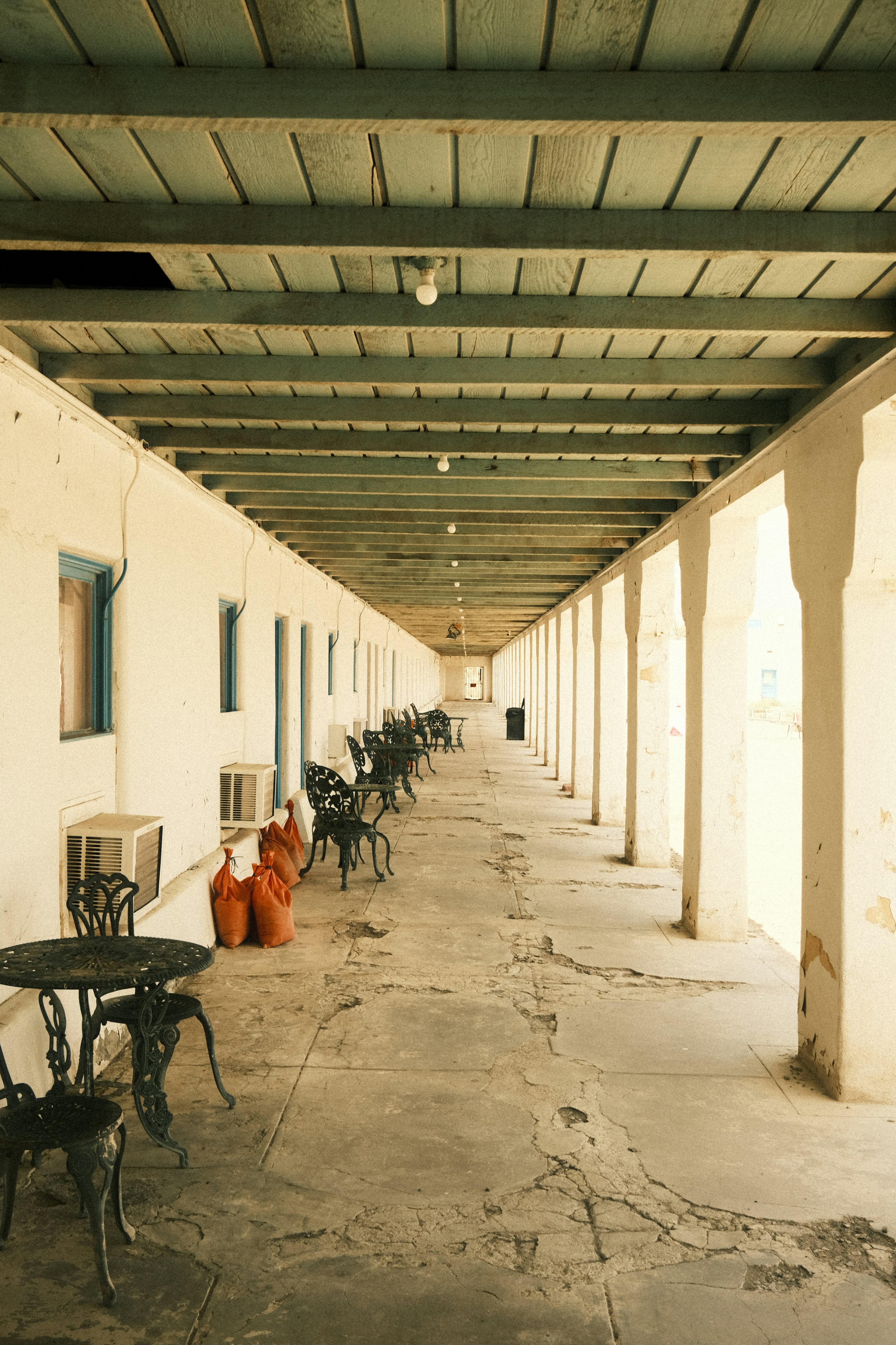 Vanishing Porch: Sunlit Colonnade with Cracked Concrete and Quiet Tables