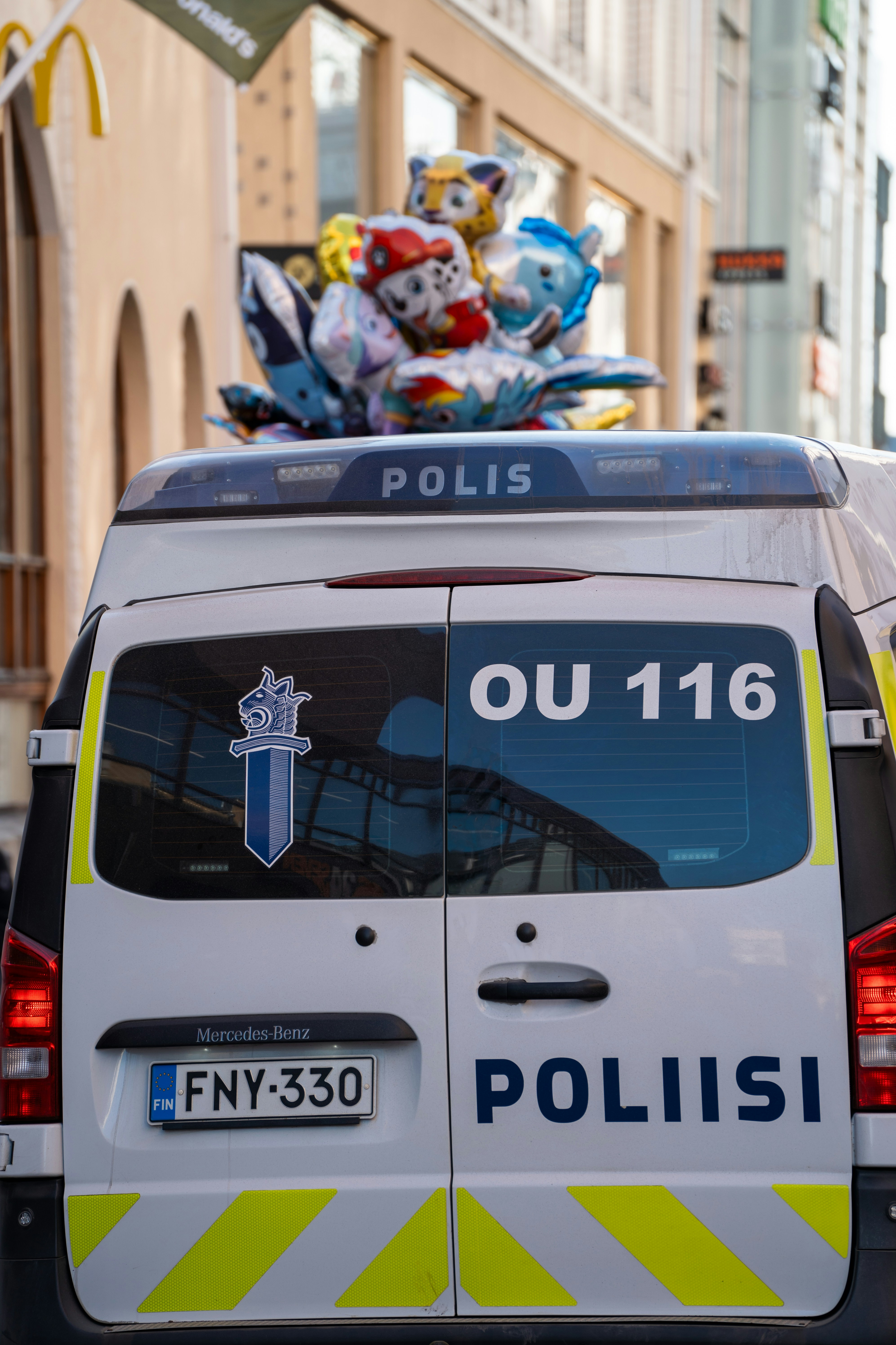 Back-Panel Portrait: A Finnish Police Van Adorned with Balloons in a Sunlit City Street