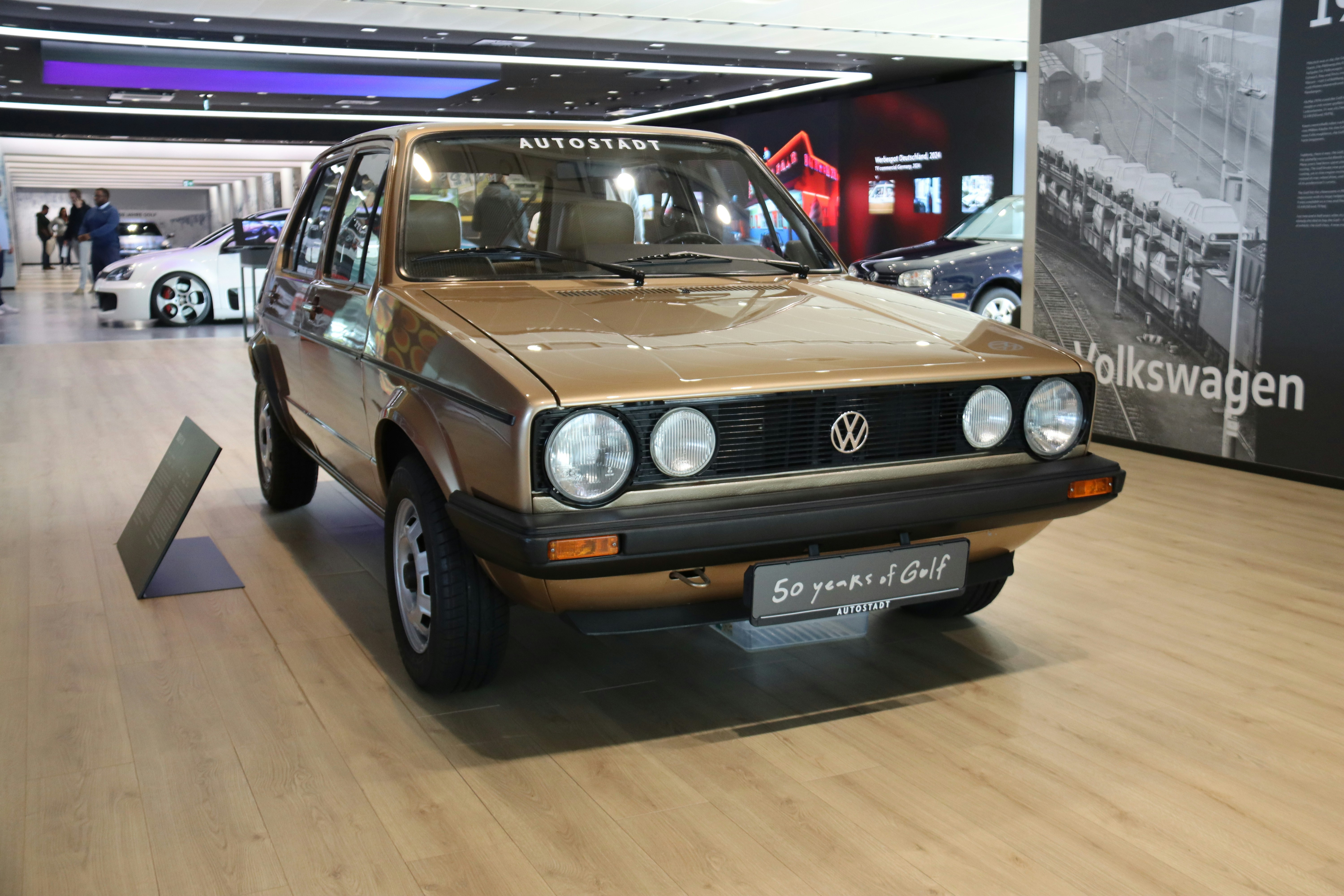 Tan VW Golf Mk2 on showroom floor, timeless lines under bright gallery lighting