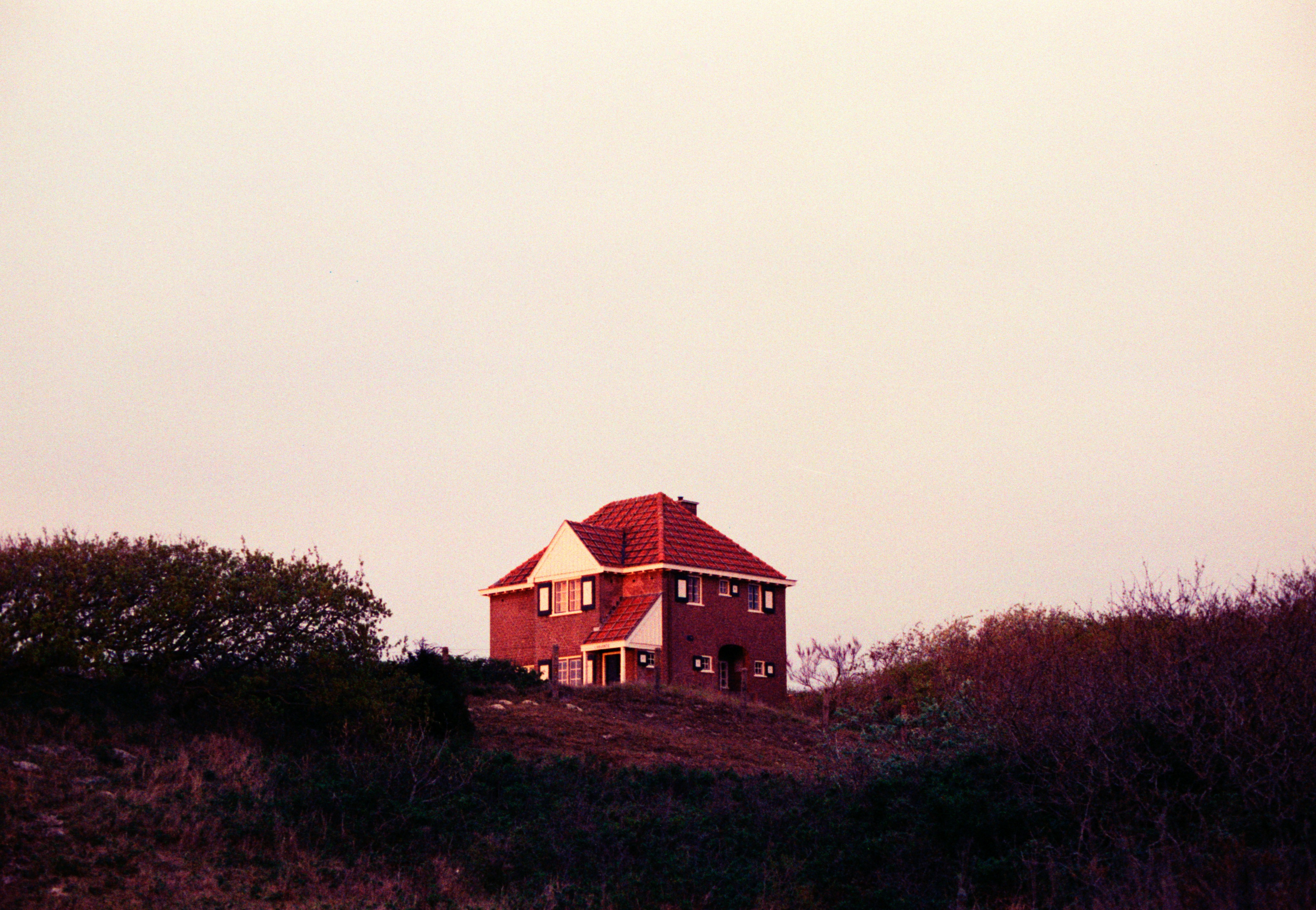 A quaint red house perched on a hill, surrounded by lush greenery under a soft pastel sky.