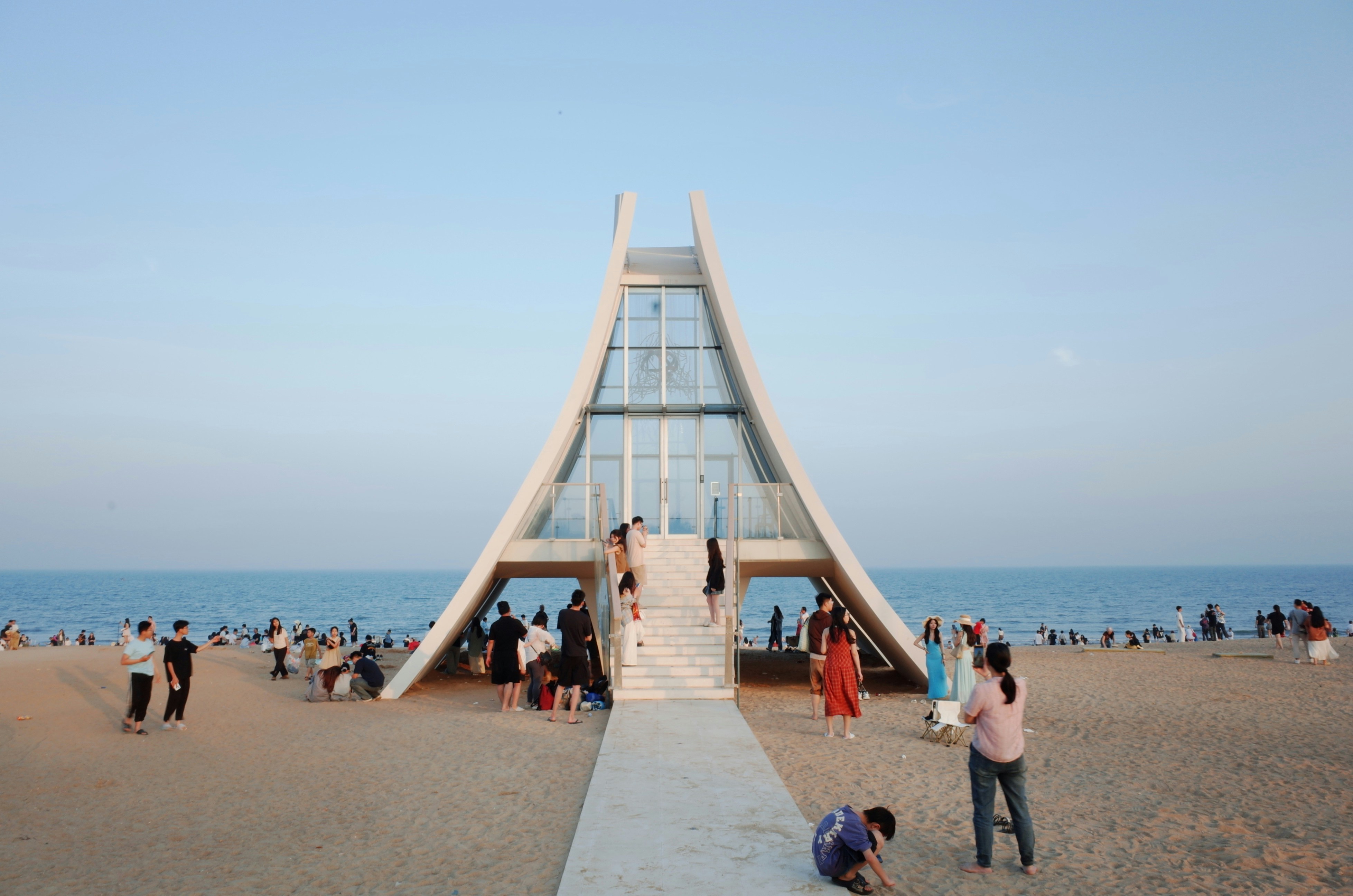 Glass Arch Over the Shore: A Modern Beach Monument Framed by Visitors