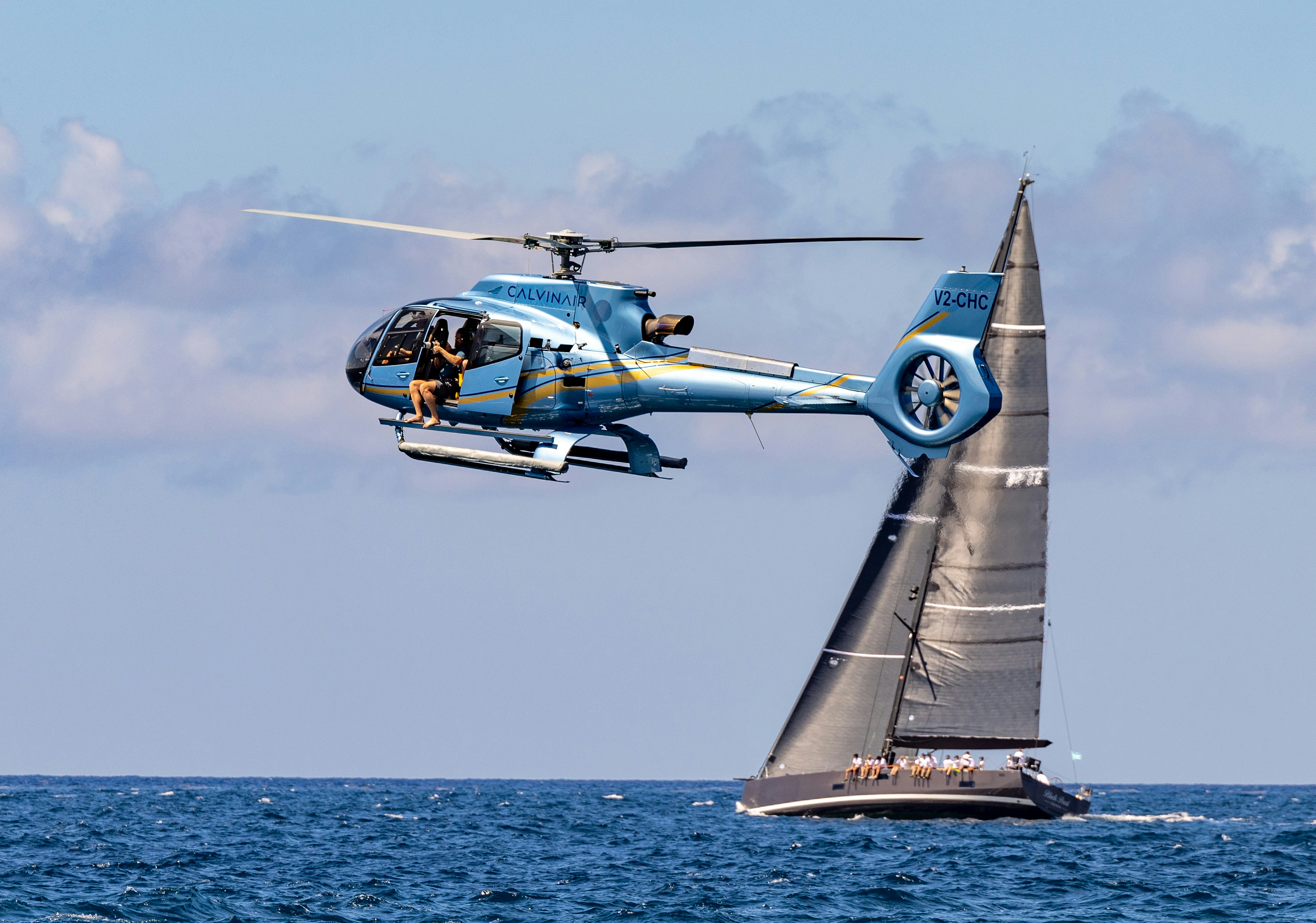 A helicopter flies over a sailboat on the ocean. photo – Free People ...